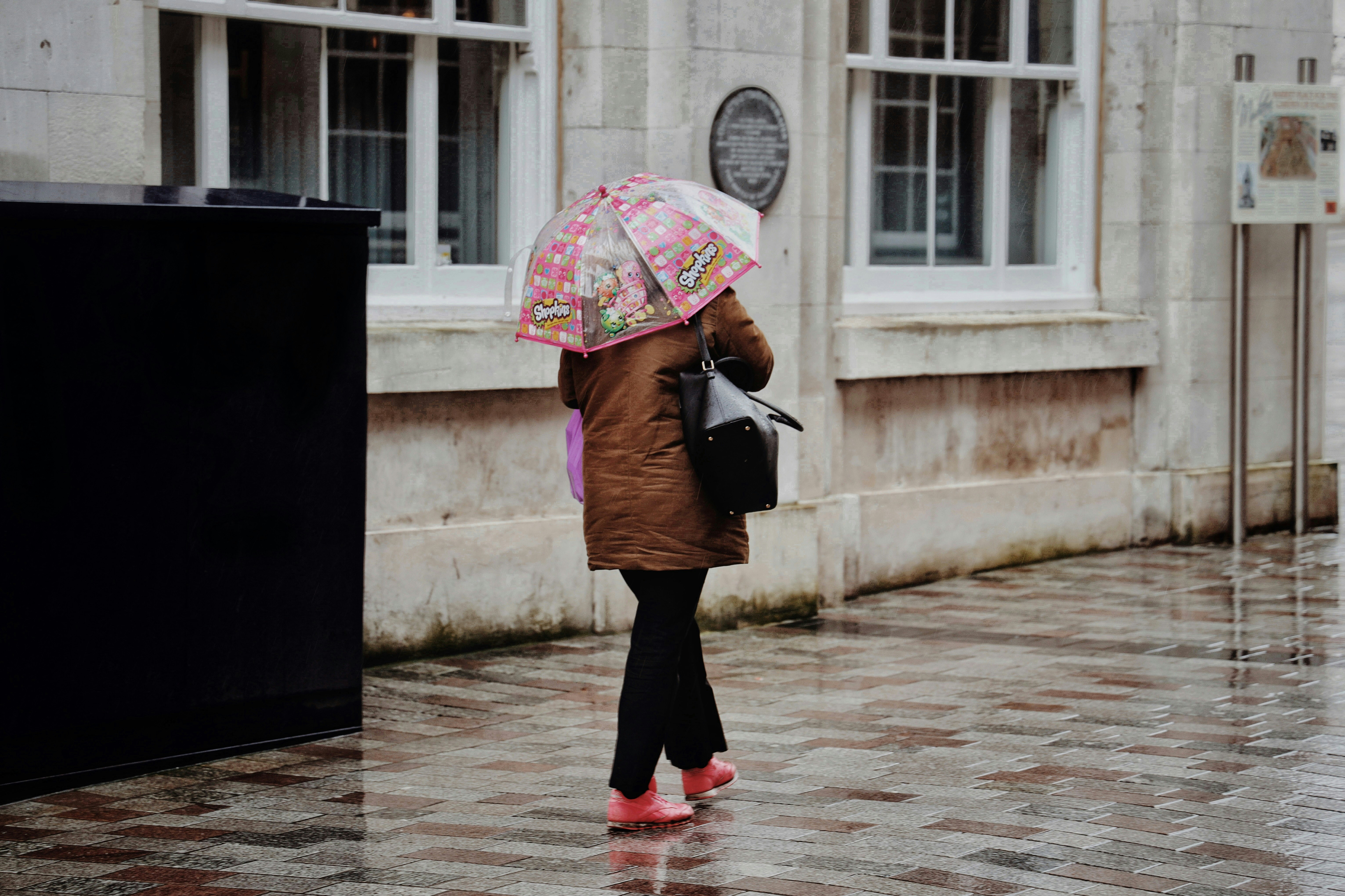 Person with a colorful umbrella walking on a wet stone pavement near a building.