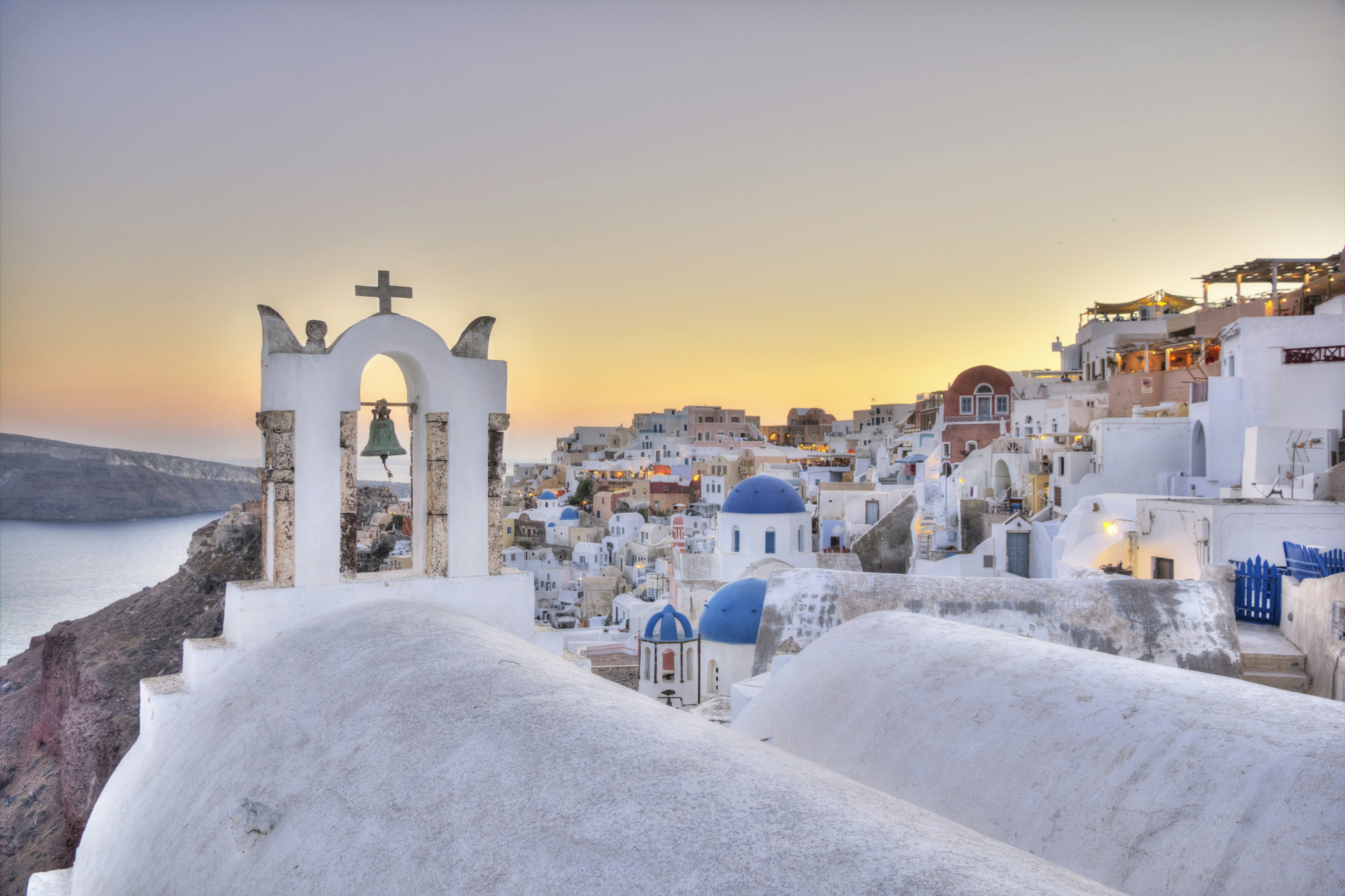 Whitewashed buildings with blue domes overlook the Aegean Sea at sunset in Oia.