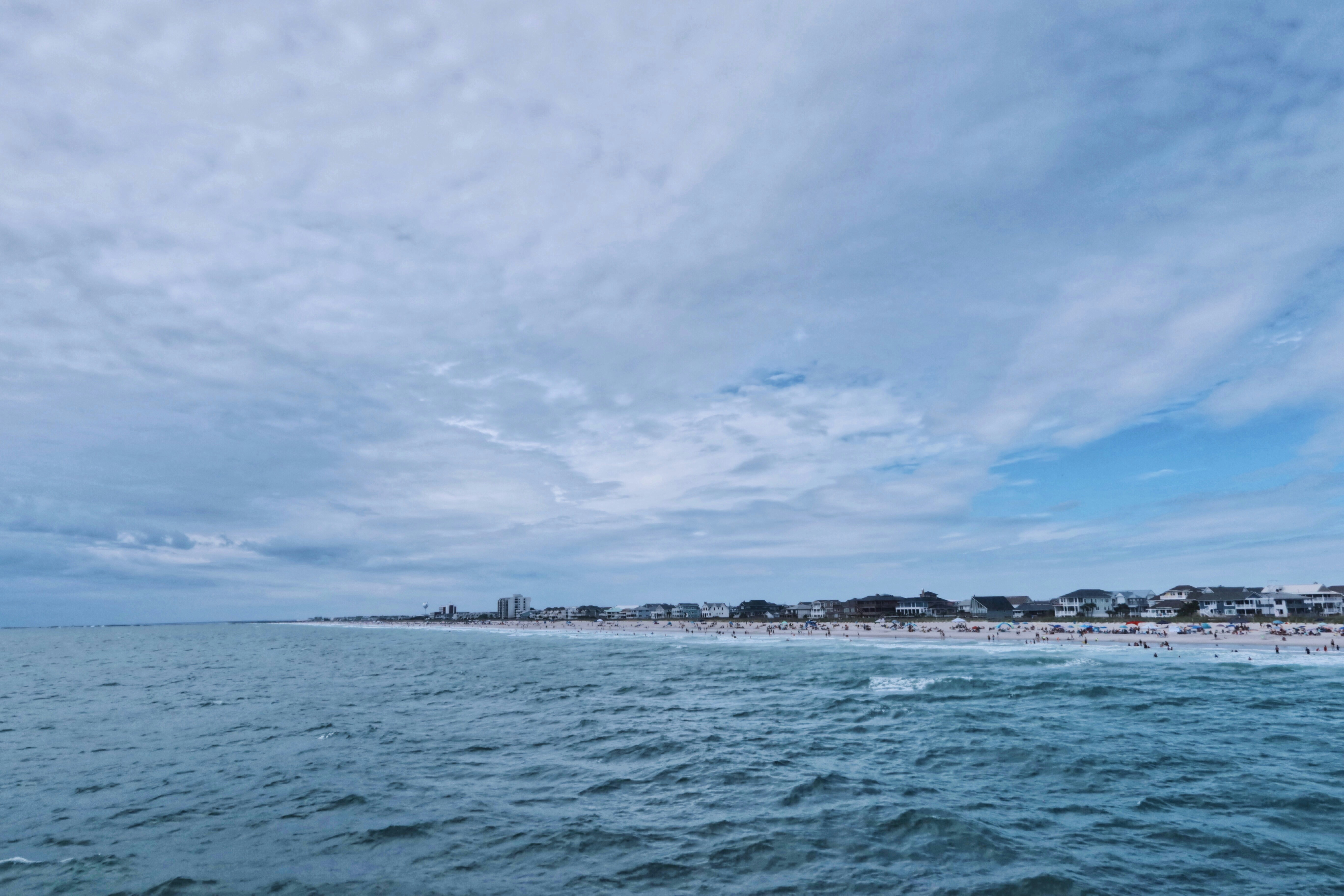 Vast ocean meeting a distant shoreline under a wide, cloudy sky.