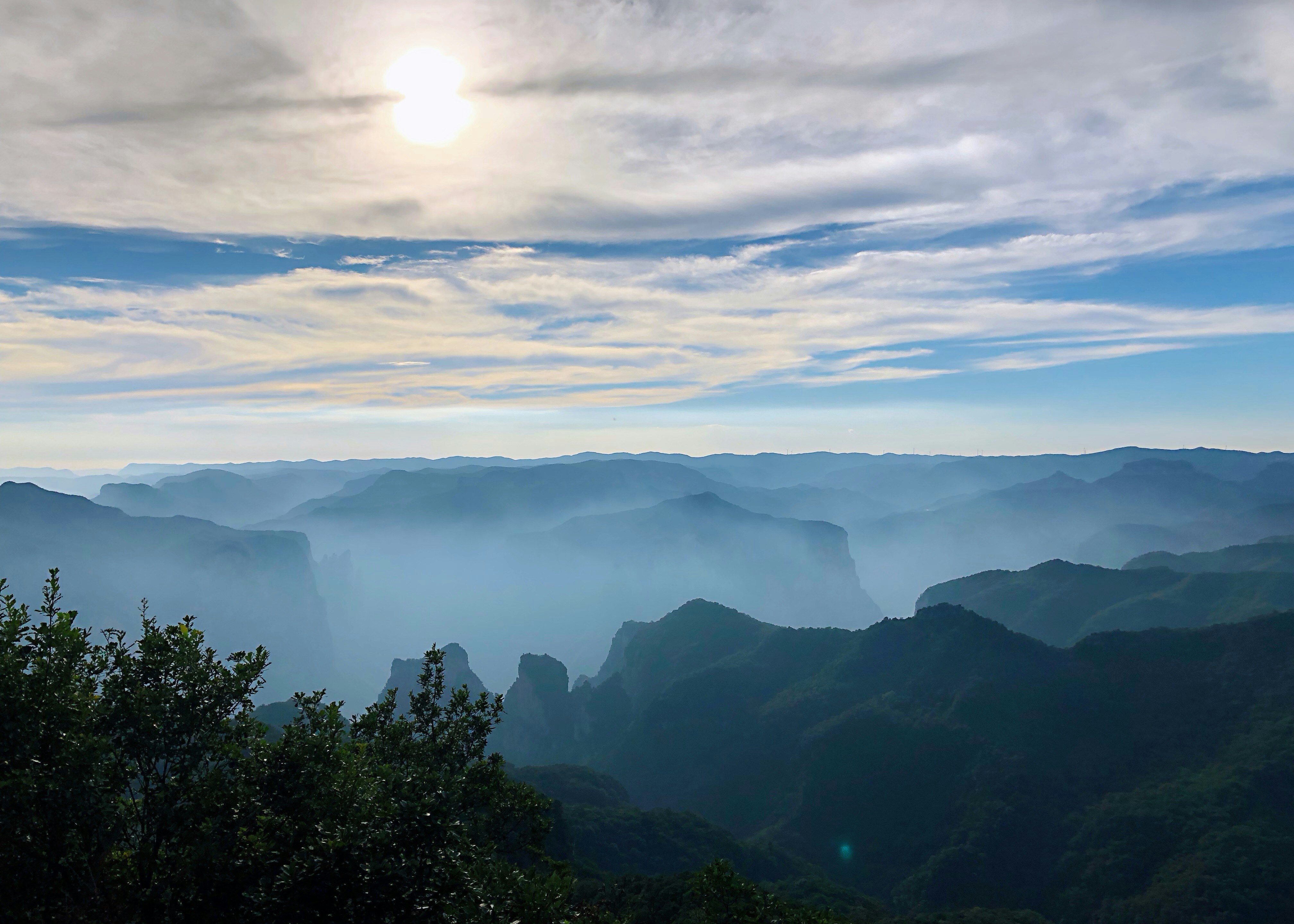 Sunlit mist envelops rolling hills under a partly cloudy sky.