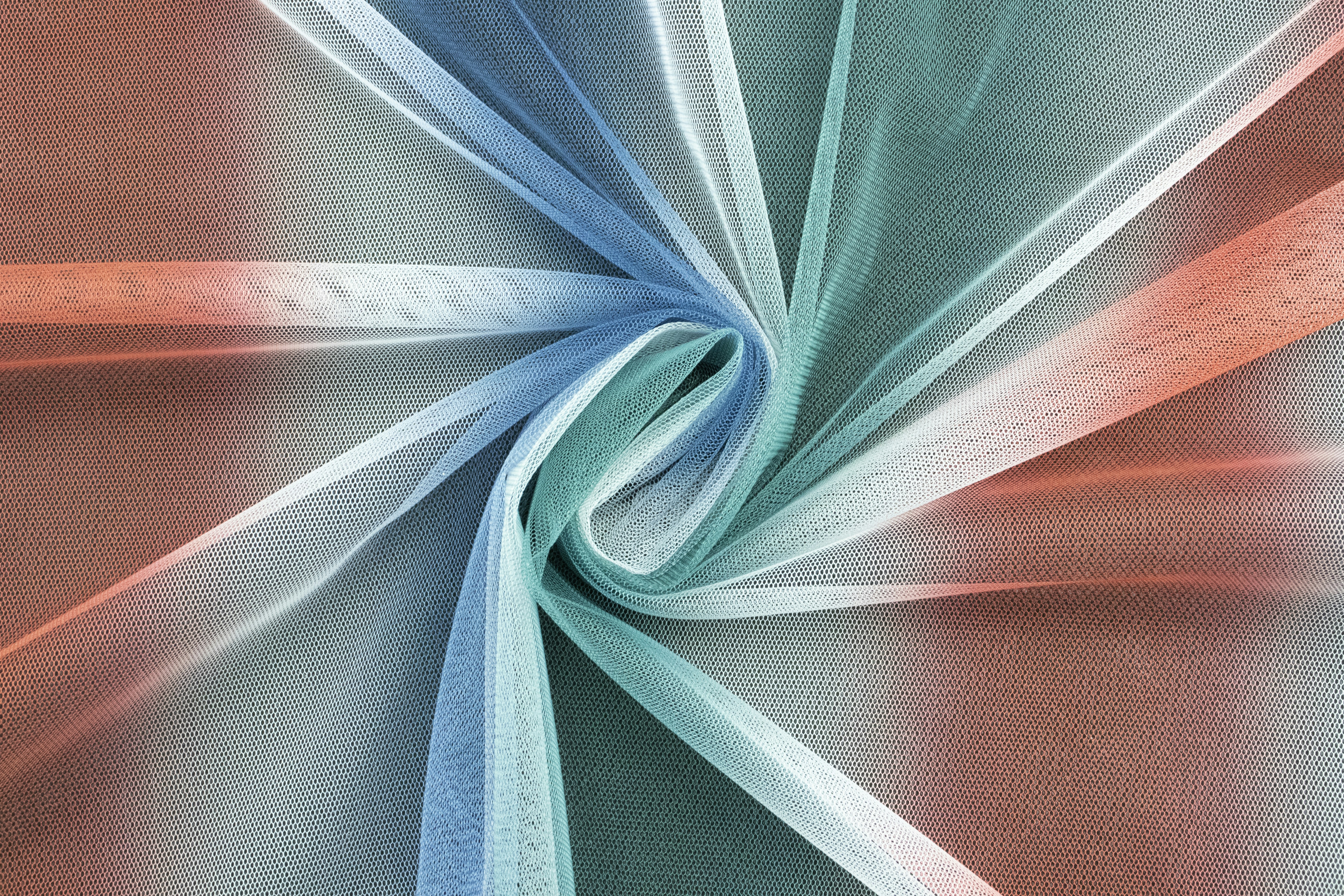 Delicate layers of sheer fabric swirl together, showcasing a blend of soft colors and textures. The interplay of light creates a mesmerizing visual effect.