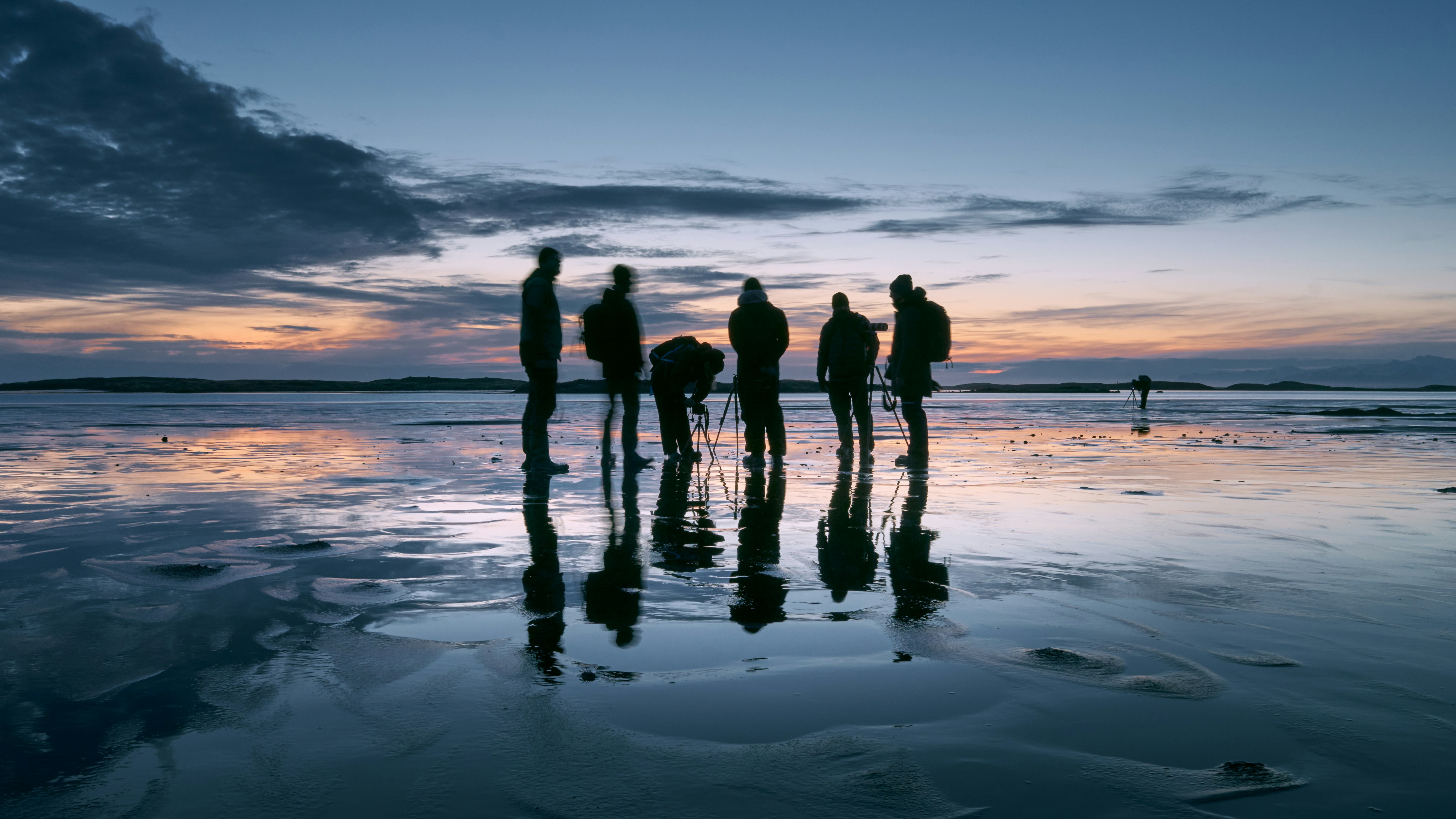 Photographers silhouetted against a reflective beach at sunset, capturing the serene beauty of the moment.