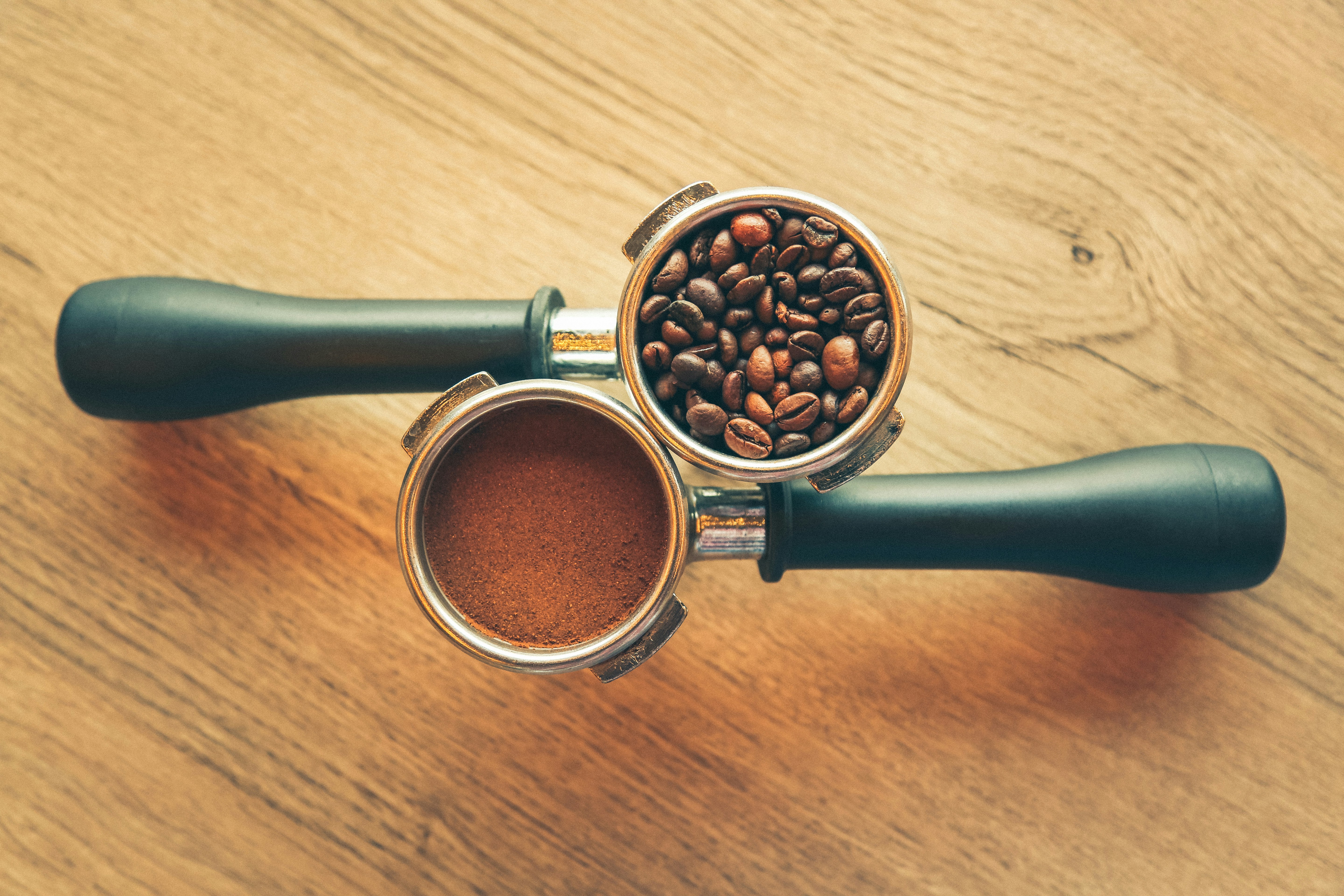 Portafilters filled with ground coffee and roasted beans on a wooden surface.