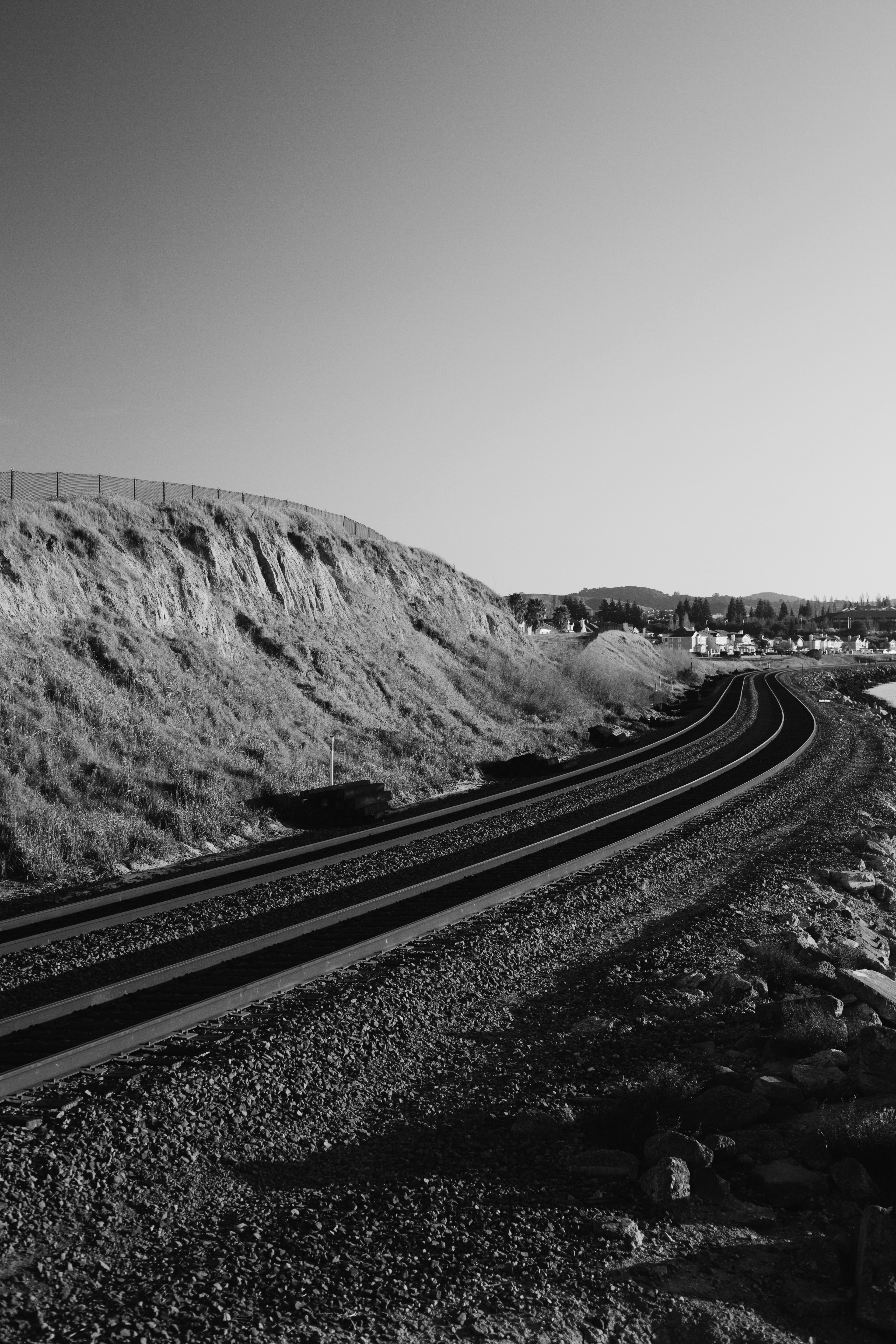 Winding railway tracks curve along a hillside, leading the eye toward a distant town under a clear sky.