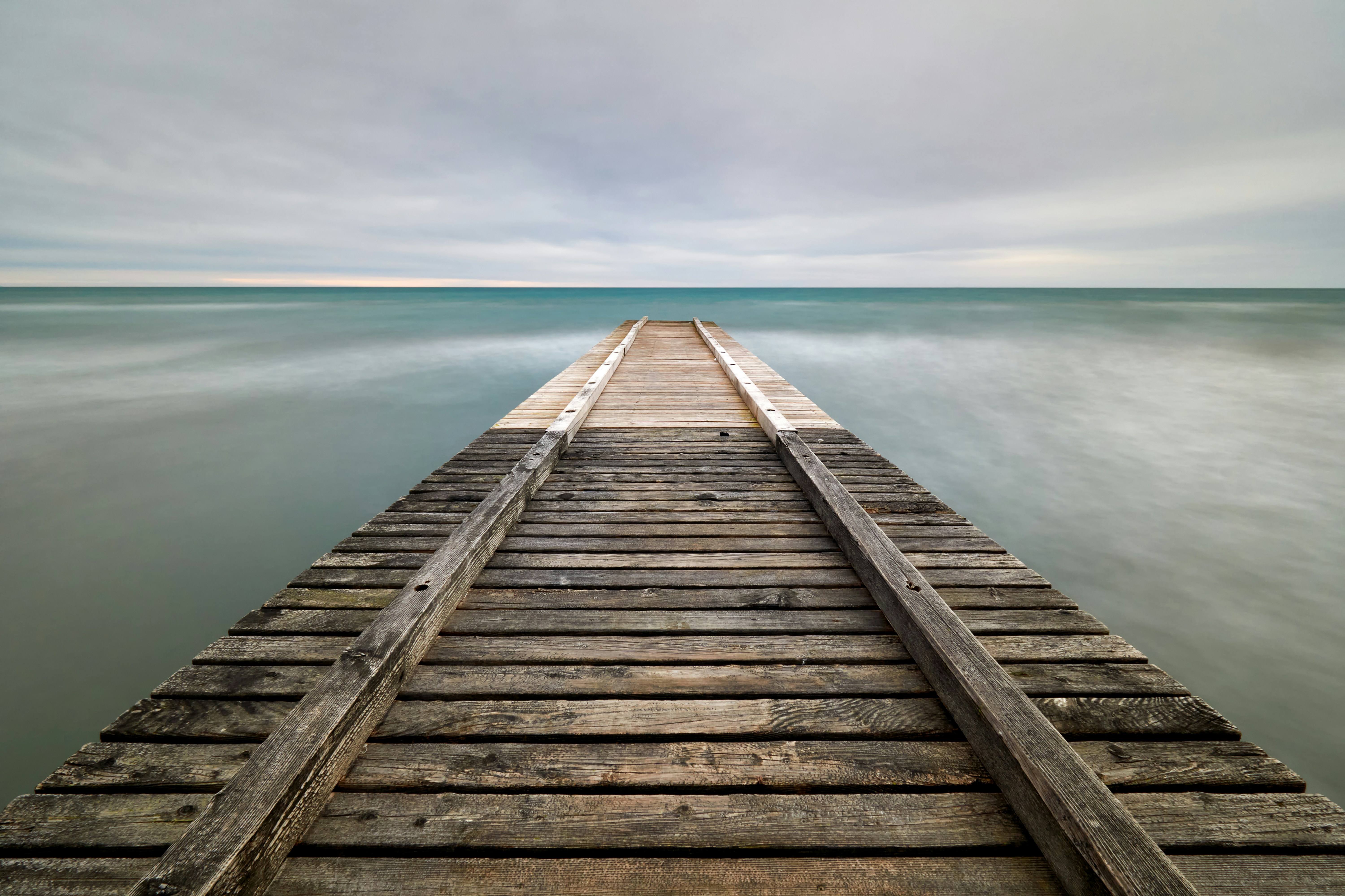 Wooden pier stretching into the calm Adriatic Sea under a cloudy sky.
