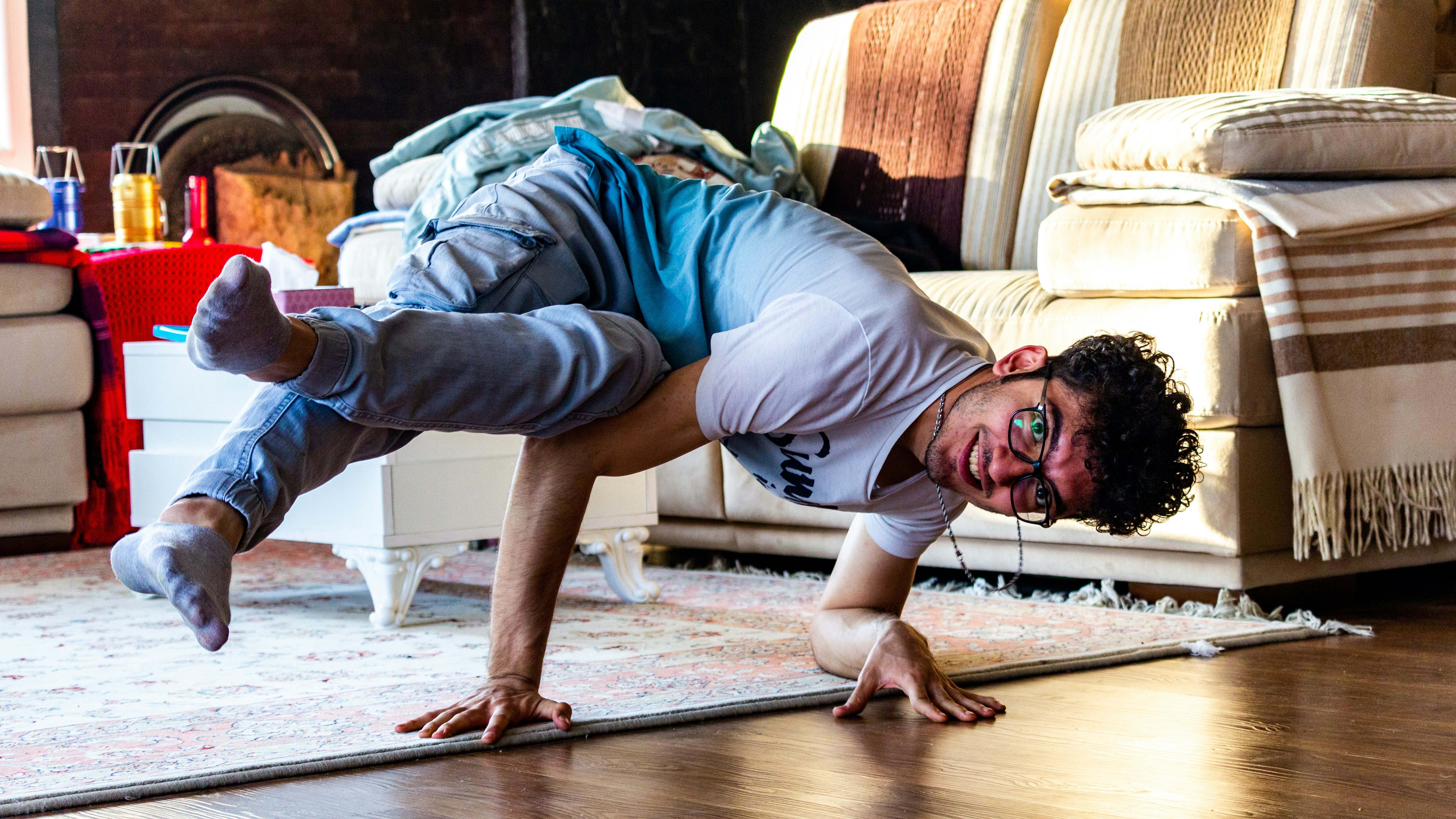 Man performing a one-handed handstand in a living room setting.