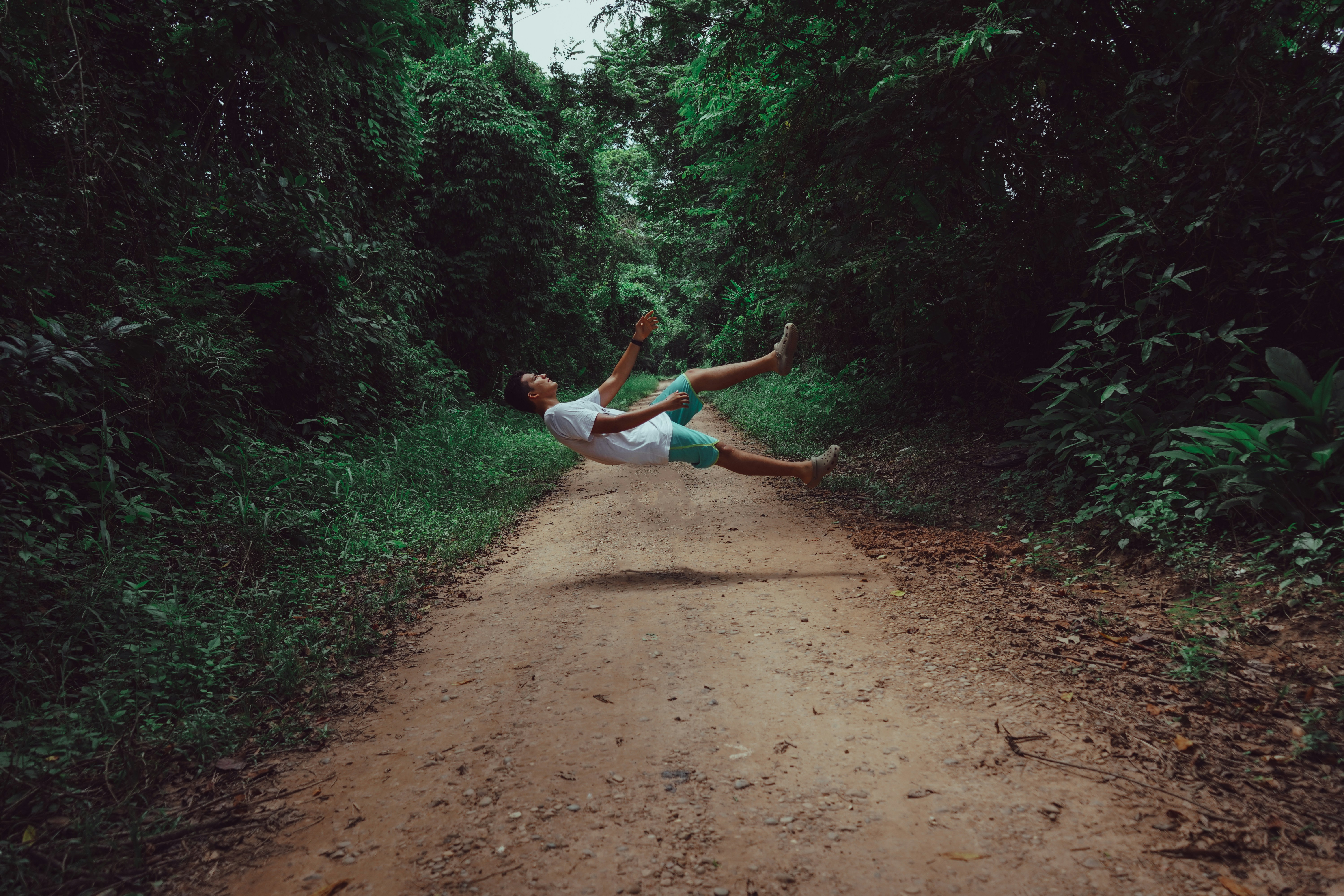 levitating in the magical jungle | woman in white tank top and white shorts jumping on brown dirt road during daytime