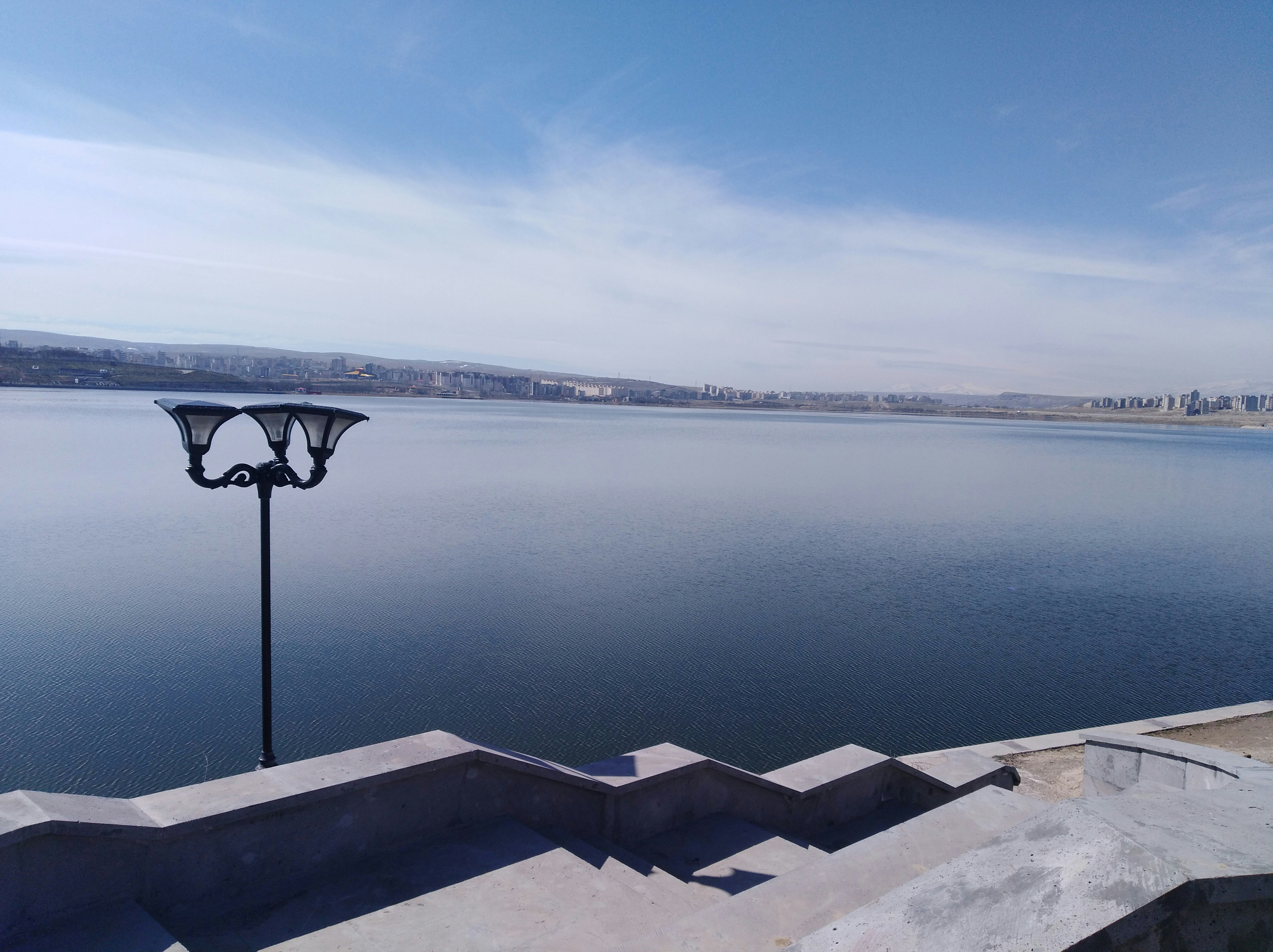 Calm lake view with a solitary lamp post and geometric stone steps under a clear blue sky.
