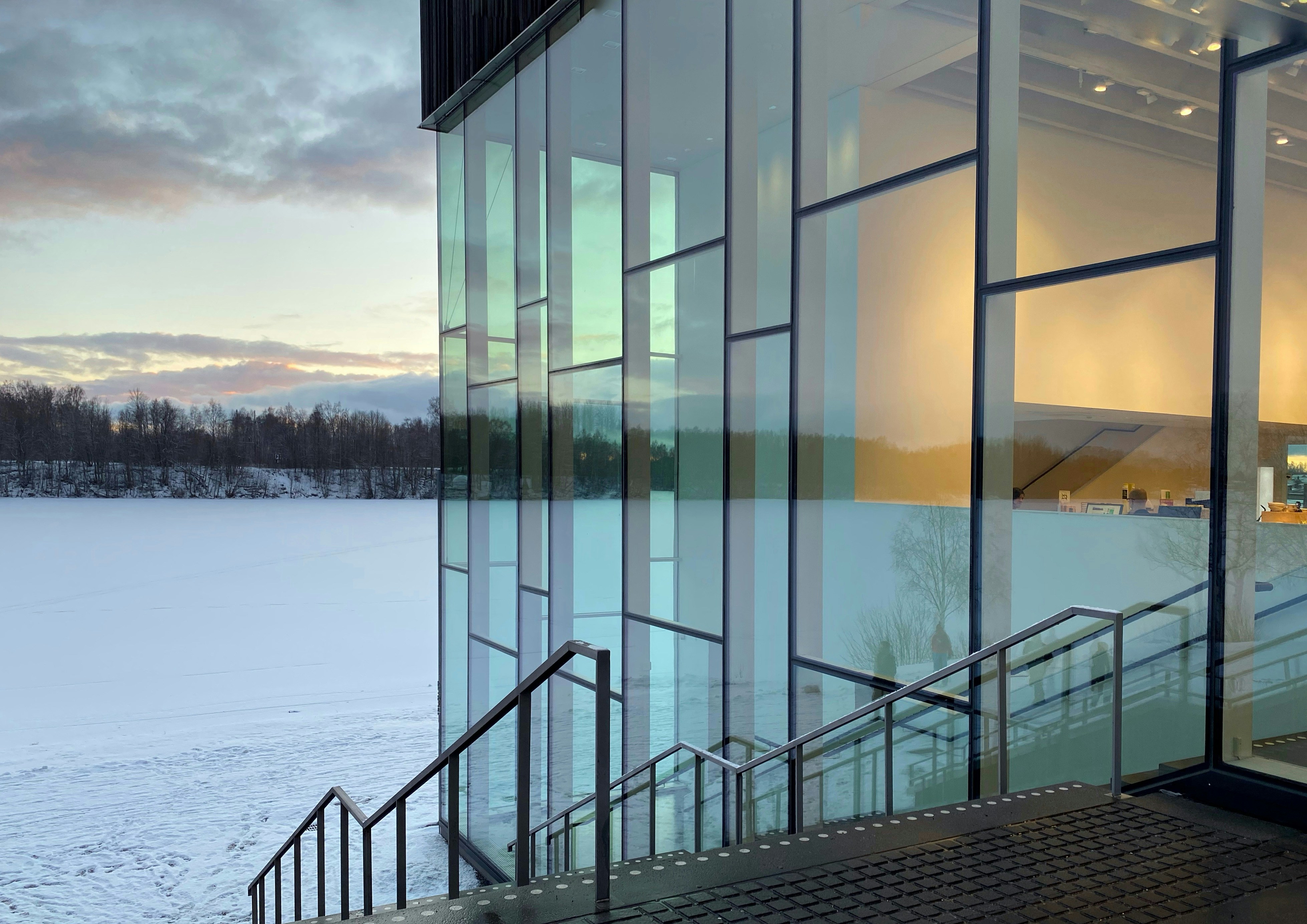 Glass Facade at Dusk: Stairs, Snow, and Sunset Reflections