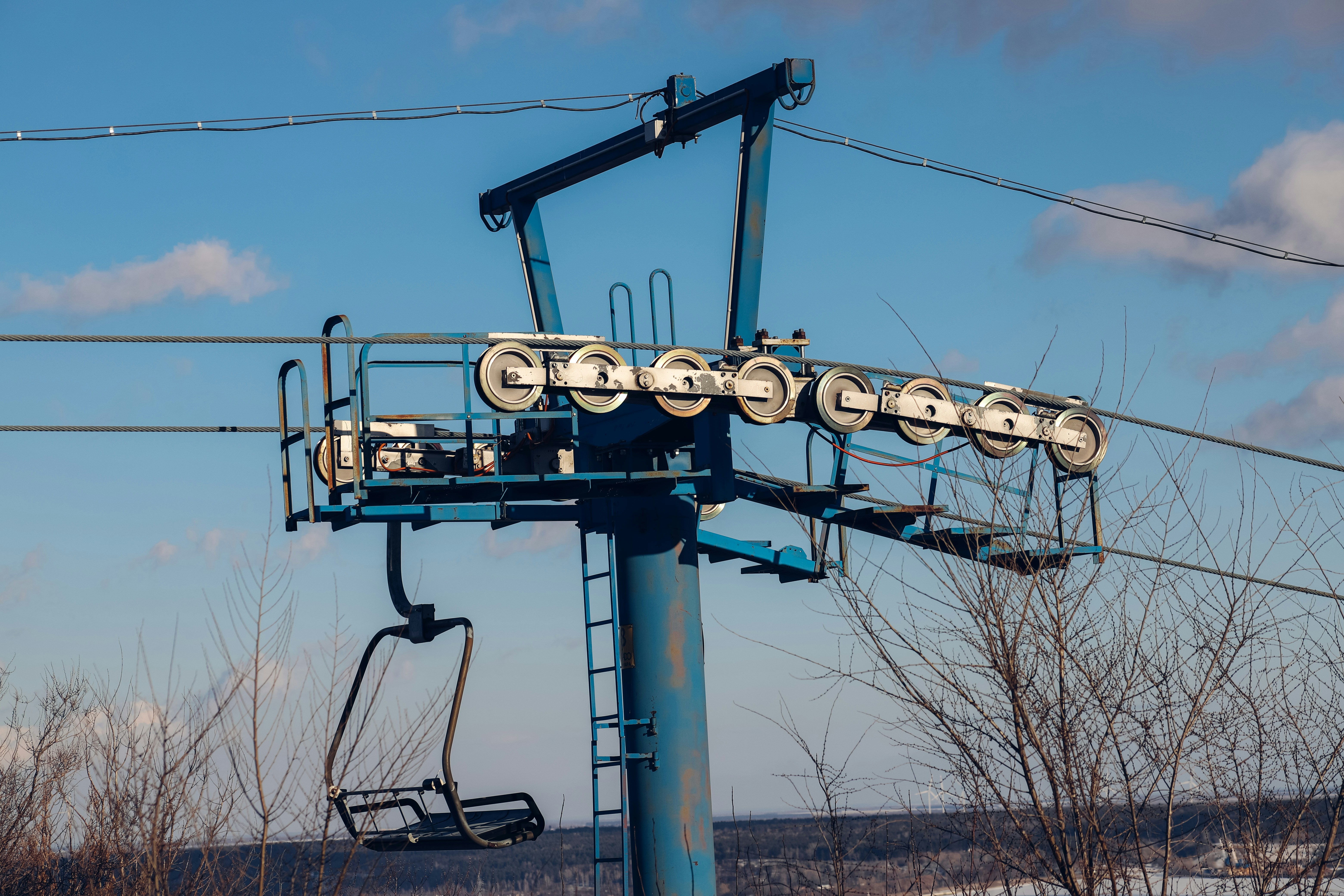 A ski lift tower stands tall against a clear blue sky, showcasing its mechanical components and the surrounding winter landscape.