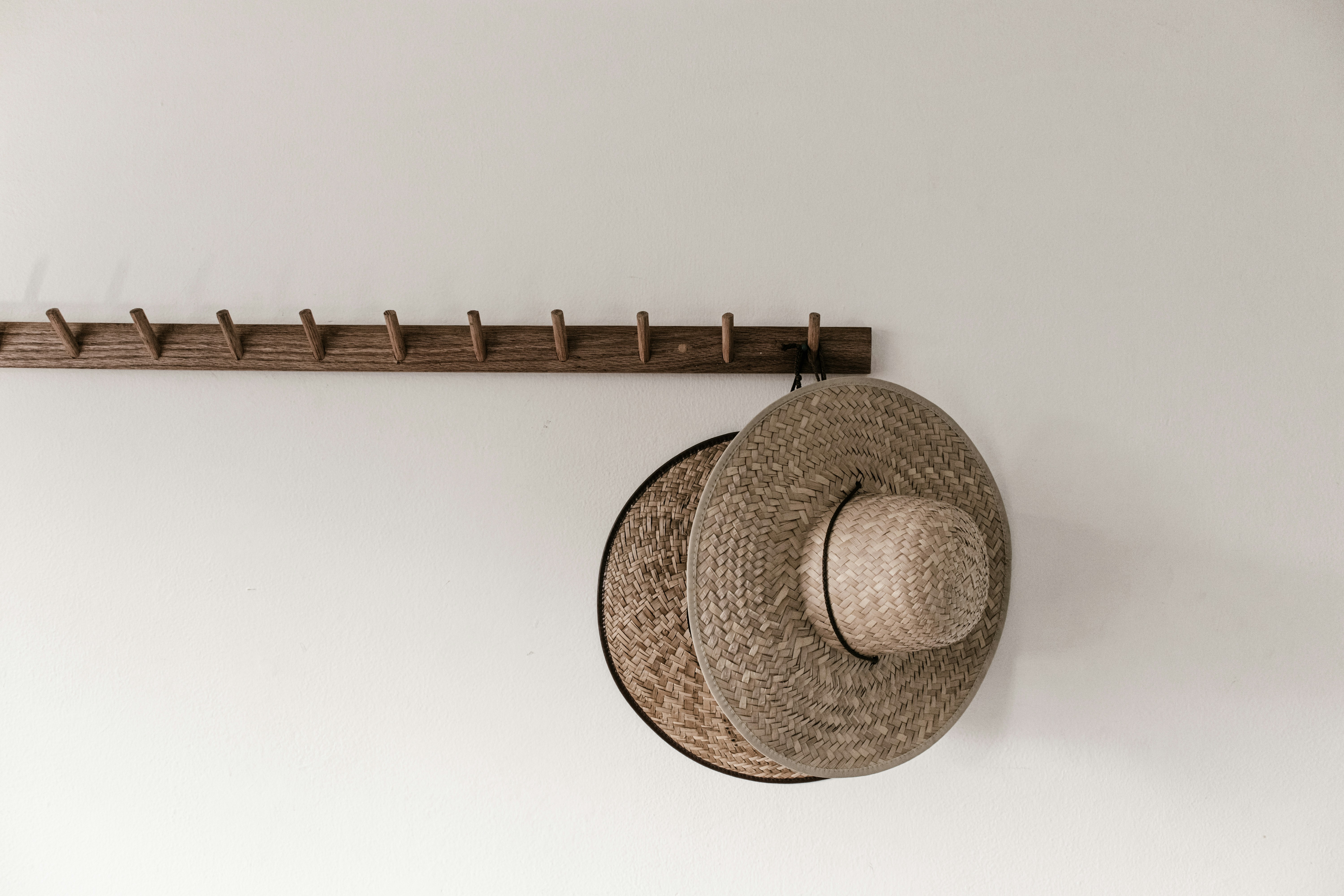 Straw hats hanging from a wooden rack against a minimalist wall, highlighting a blend of functionality and aesthetic appeal.