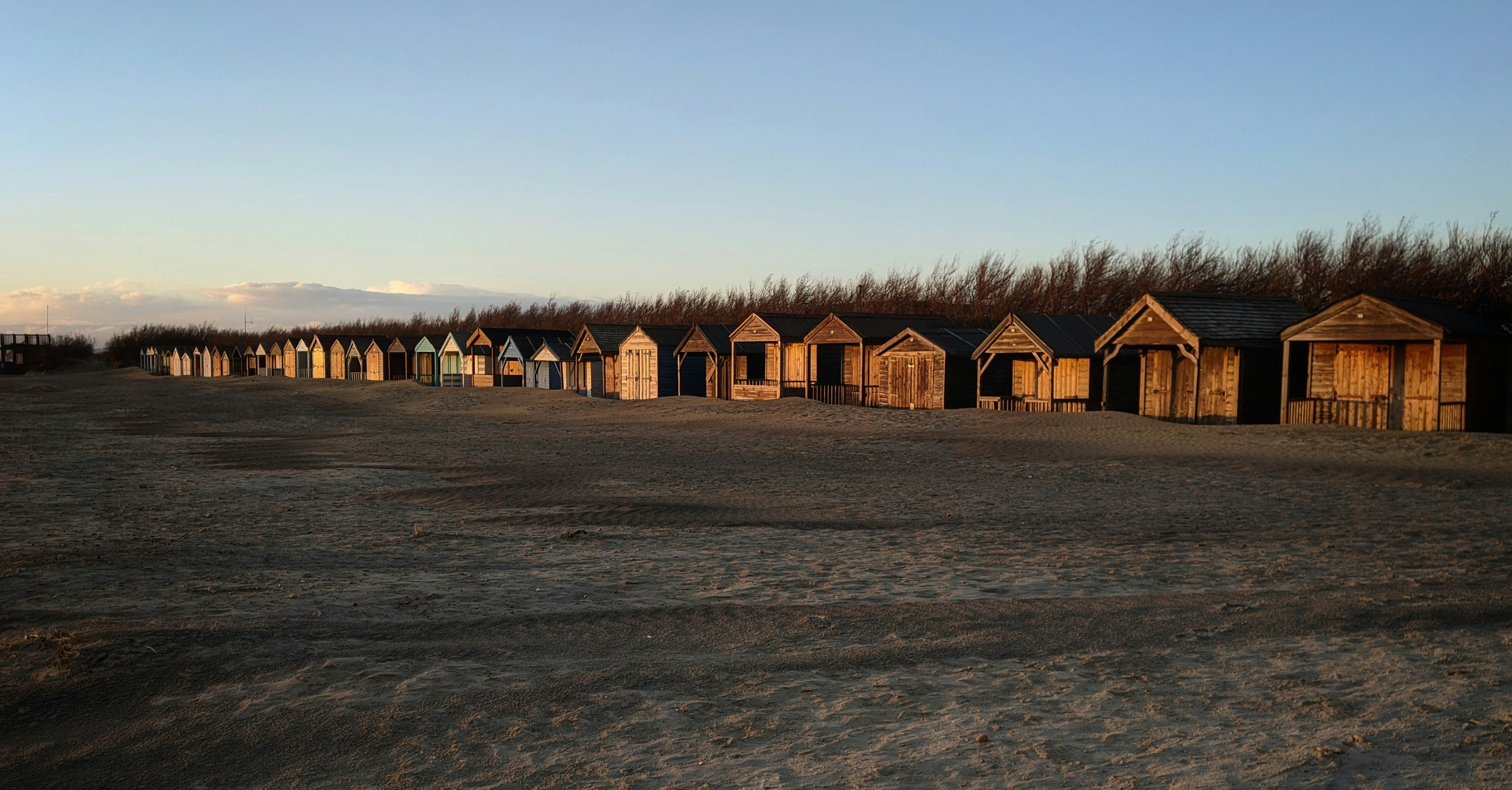 Charming beach huts line a sandy shore, illuminated by the warm glow of sunset. The scene captures the tranquility of coastal living.