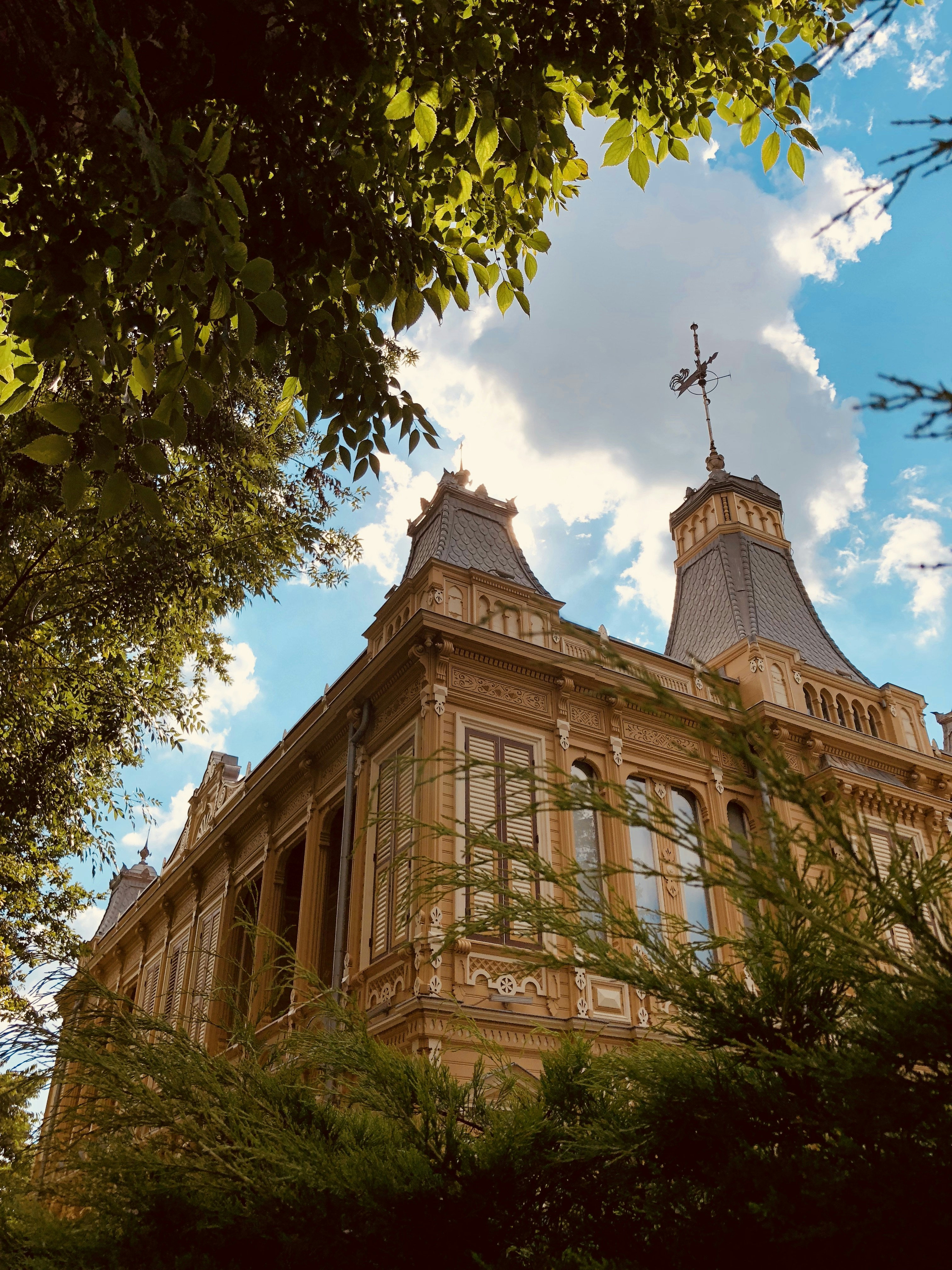 Historic building framed by lush greenery and dramatic clouds above, showcasing intricate architectural details. 