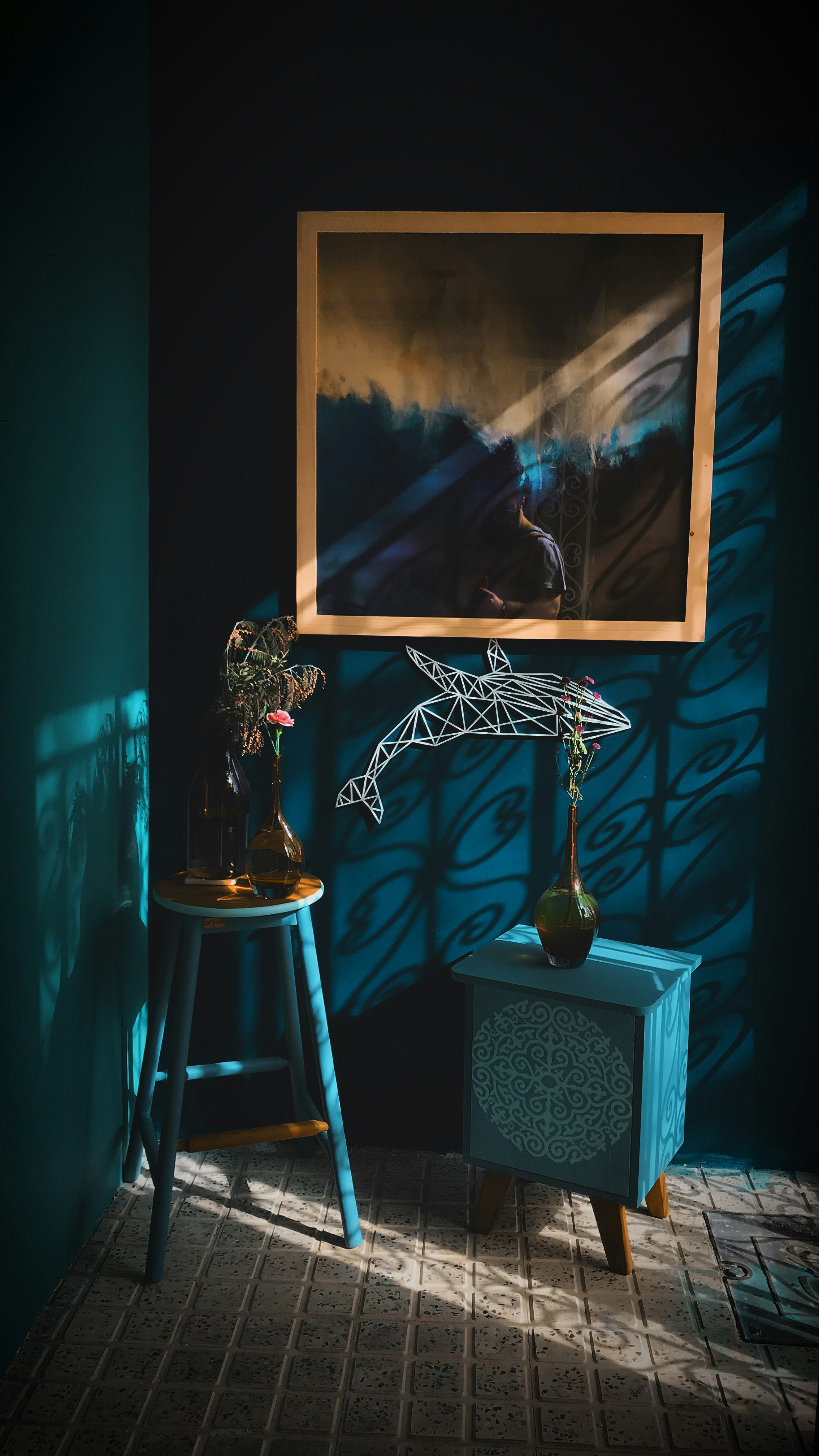 Geometric whale sculpture and vases with dried flowers in a cozy nook, illuminated by soft light casting intricate shadows on the wall.