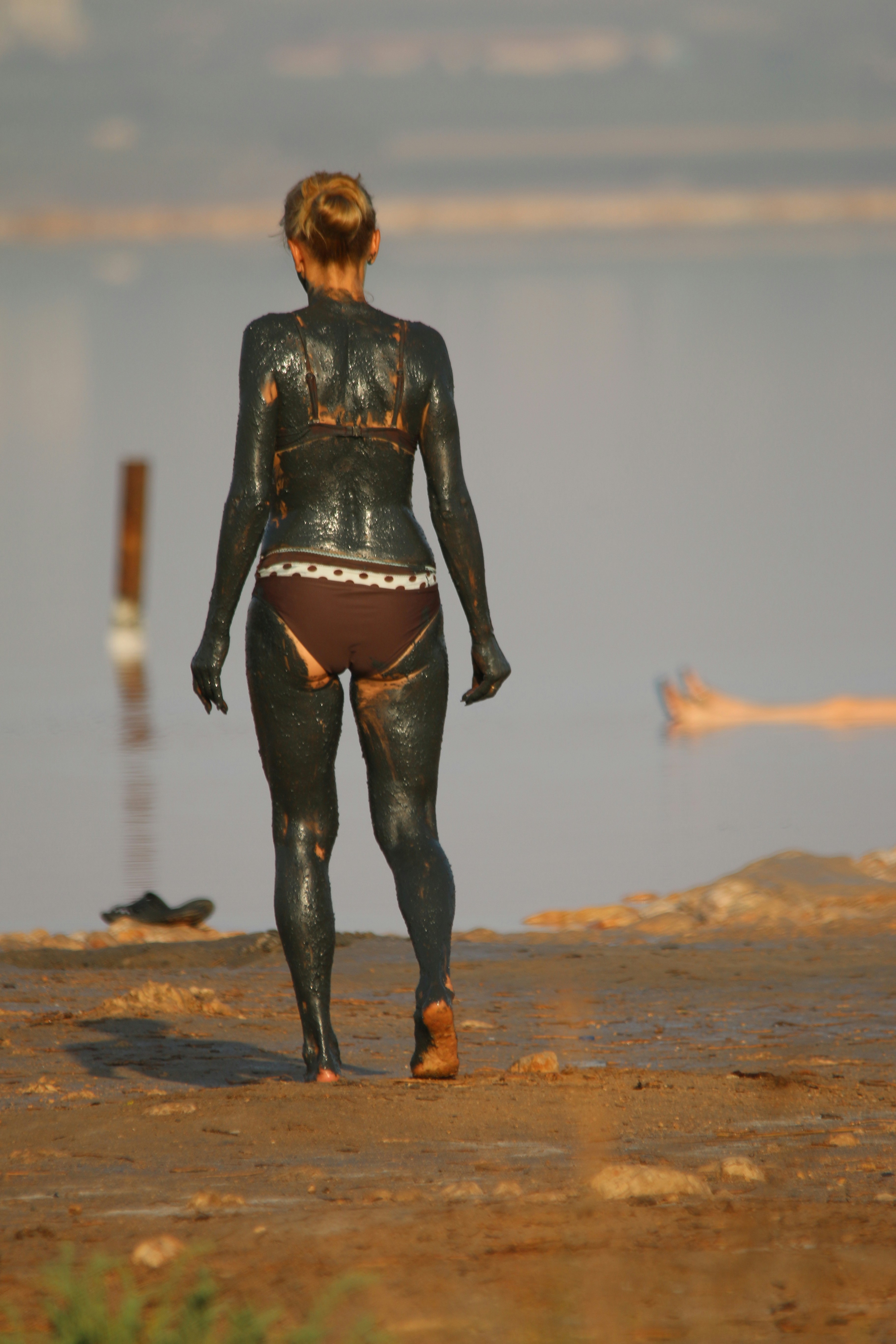 Mud-slicked silhouette strides along a sunlit shoreline