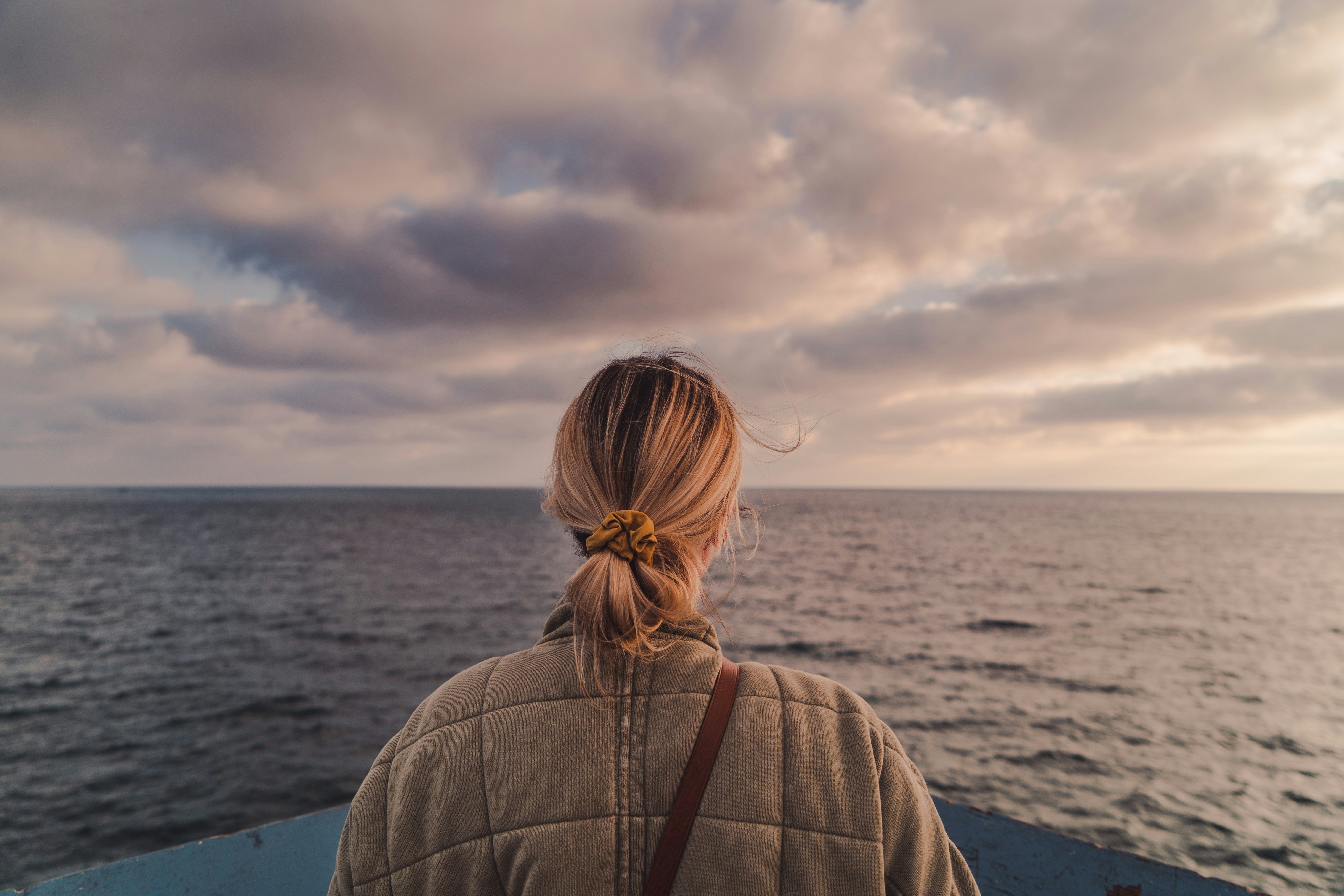 Person gazes over the Pacific Ocean from San Clemente Pier under a cloud-streaked sky.