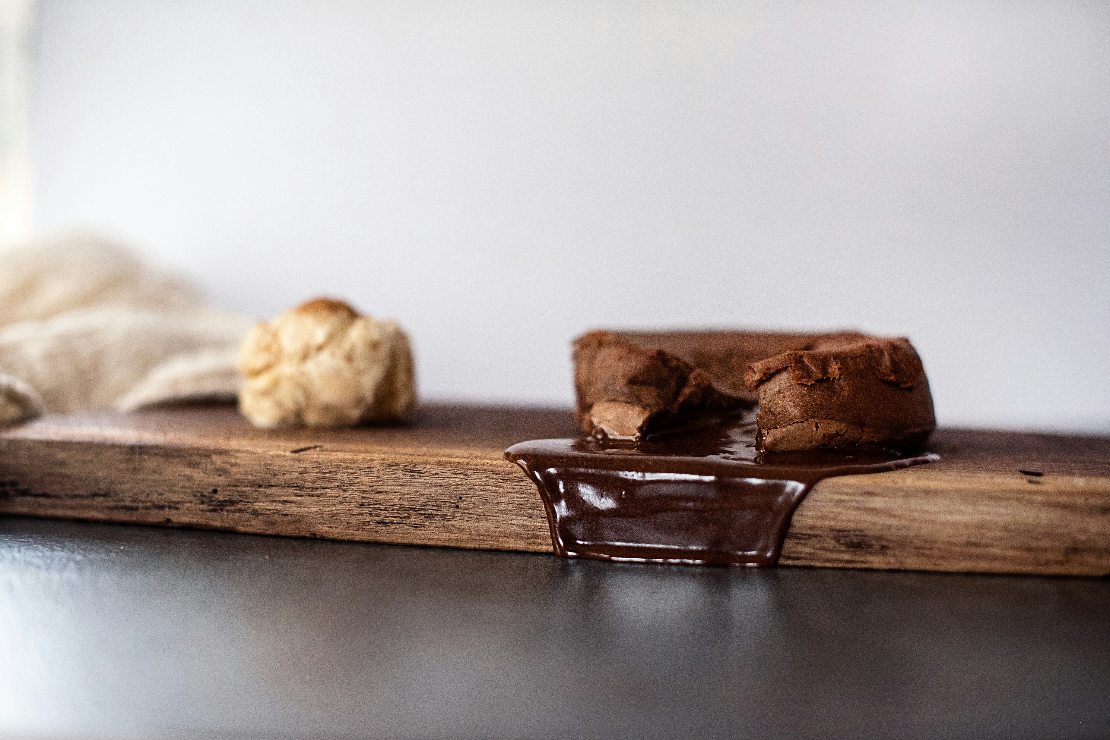 Chocolate dessert with a glossy sheen on a wooden board, accompanied by a pastry roll.