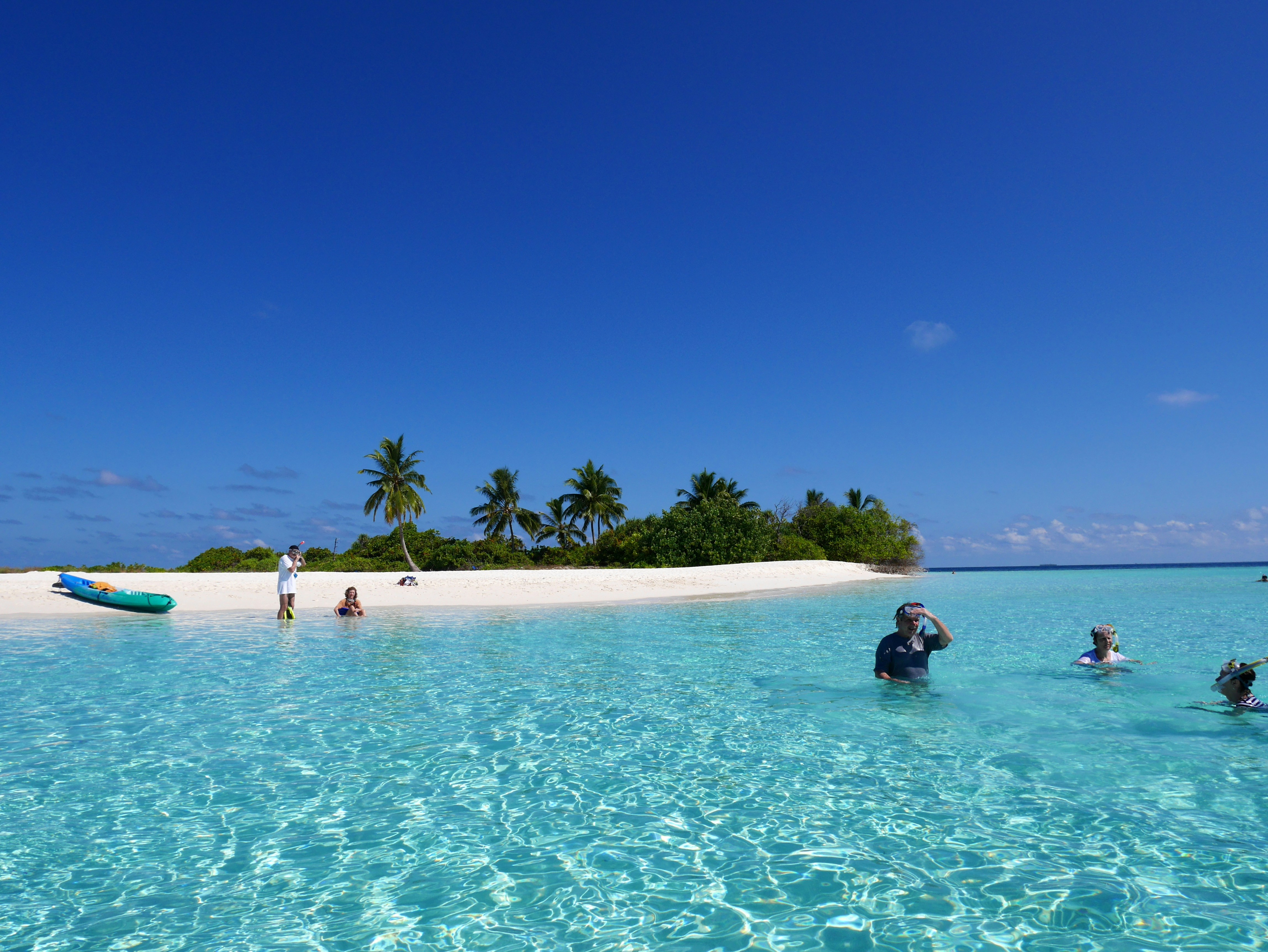 Tourists enjoying a tranquil day in the clear blue waters of a tropical paradise, with a sandy beach and lush palm trees in the background.