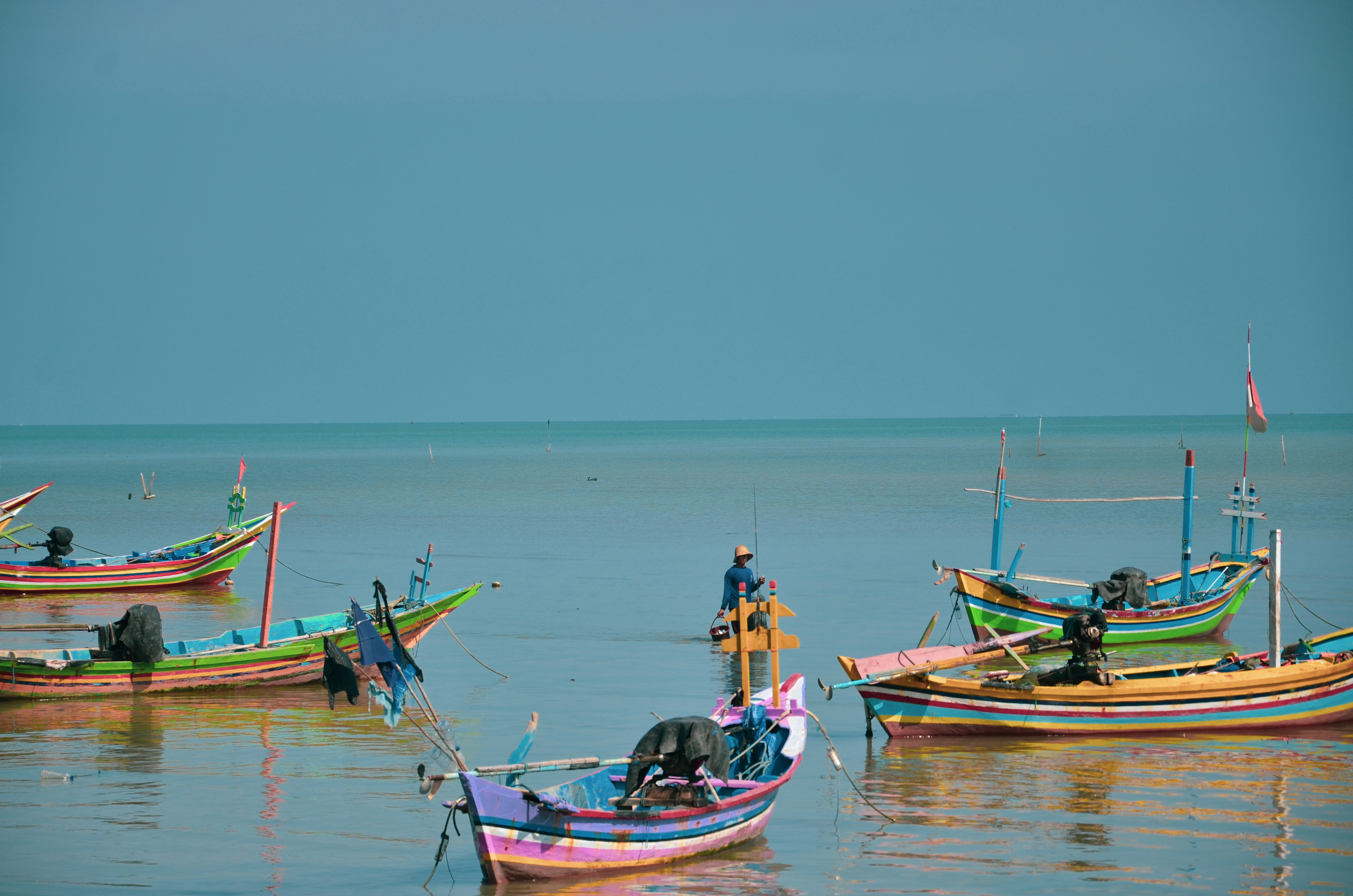 Colorful fishing boats gently floating on a calm sea under a clear blue sky.