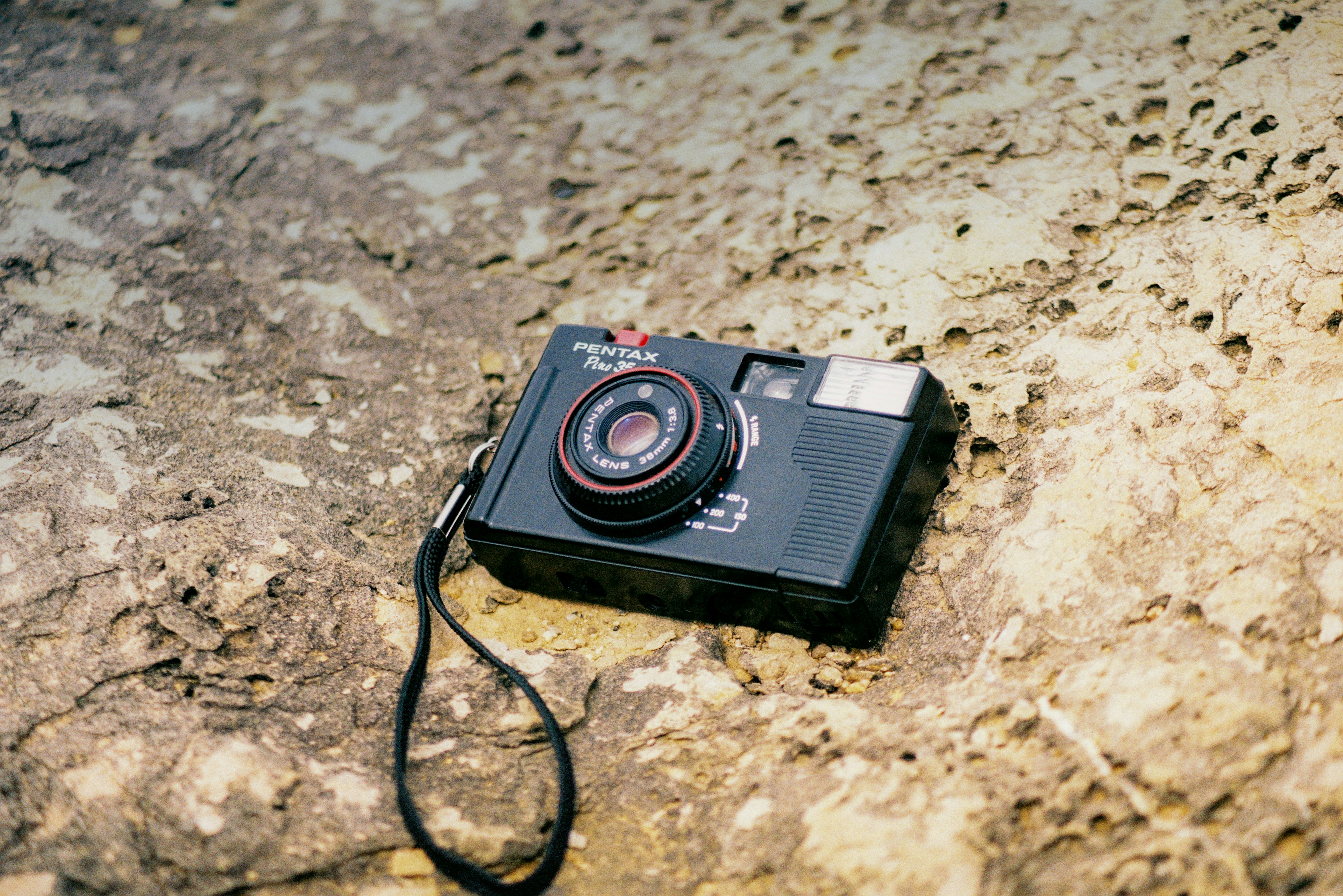 Pentax camera resting on a textured surface, showcasing its classic design and craftsmanship.
