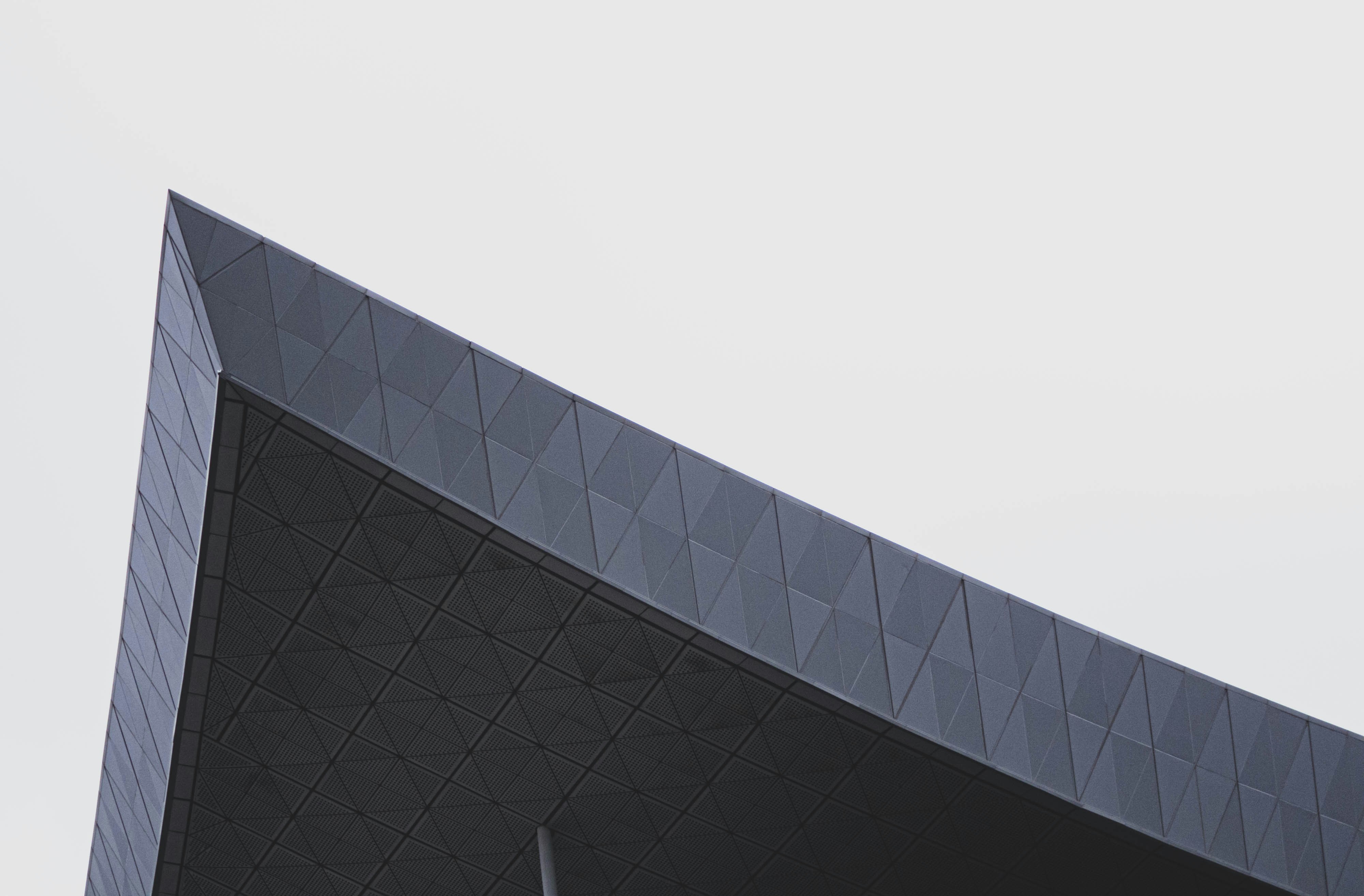 Sharp, angular roofline of a contemporary building against a pale sky, emphasizing geometric patterns and minimalist design.