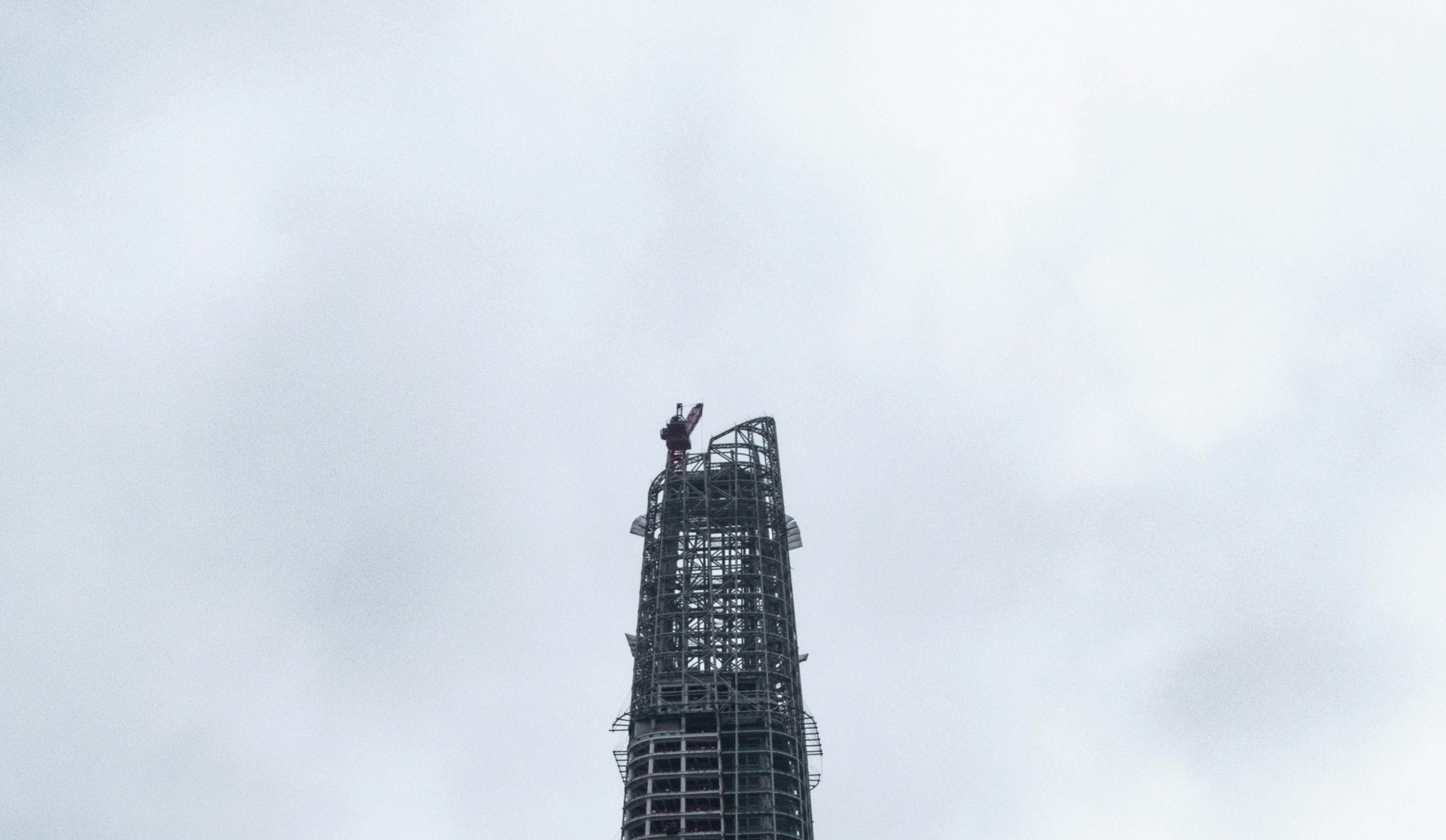 Construction worker perched atop a skyscraper framework under a cloudy sky.