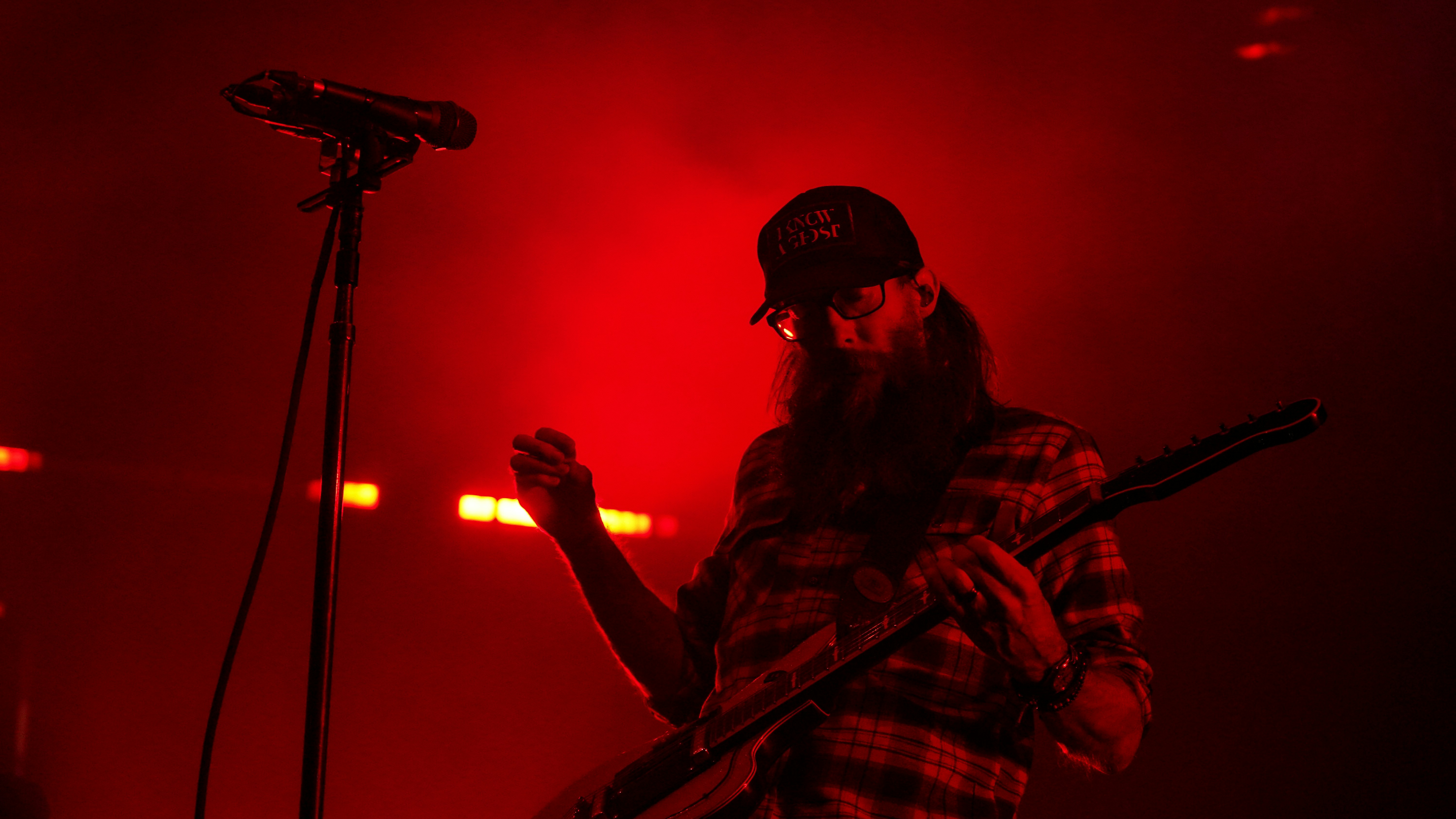 Musician with a guitar illuminated by dramatic red lighting on stage, creating an intense atmosphere.