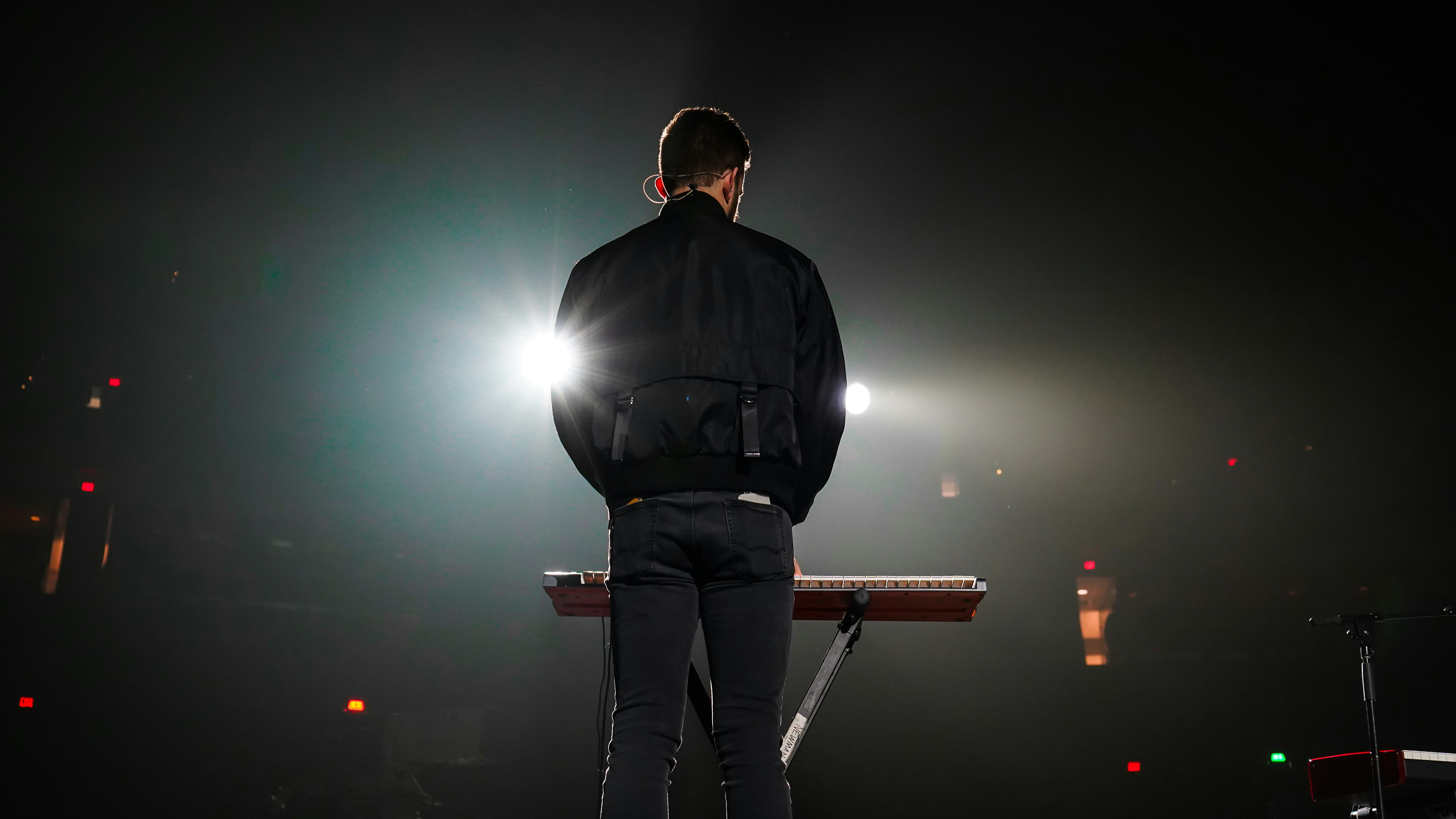 Musician stands at a keyboard, illuminated by dramatic stage lights, creating a captivating atmosphere of anticipation.