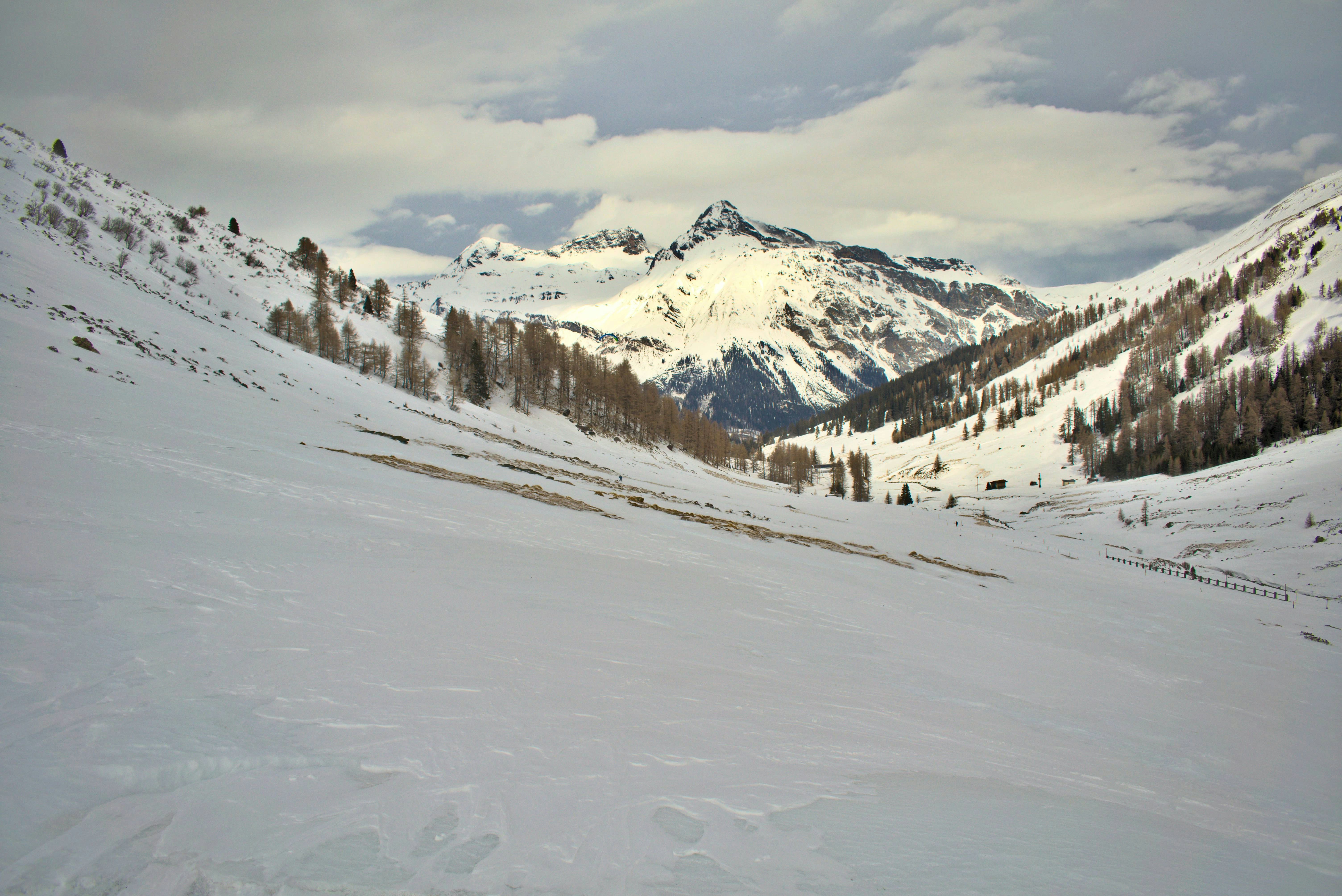 Snow-covered valley framed by majestic mountains under a cloudy sky. The scene captures the serene beauty of a winter landscape.