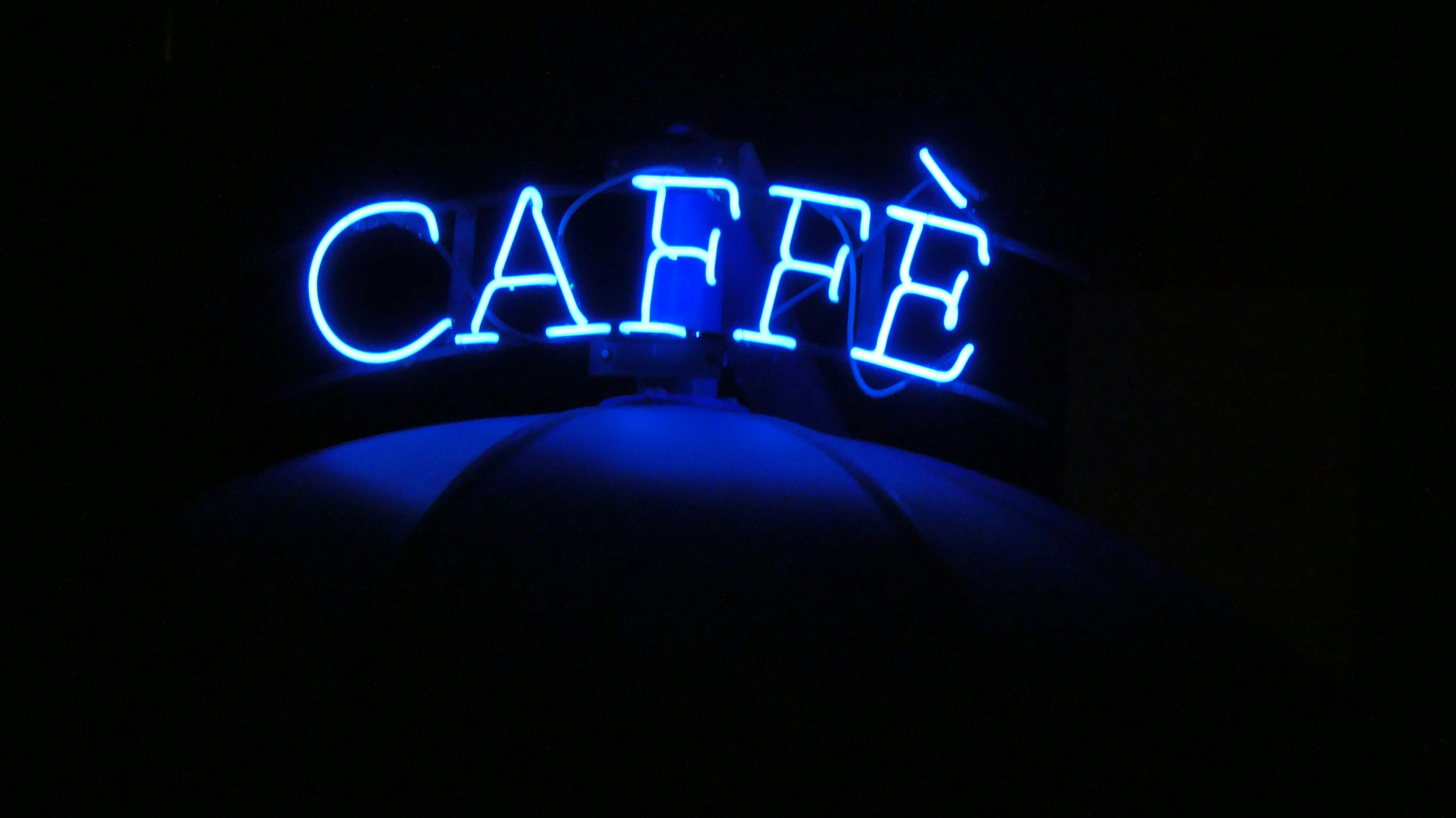 Illuminated blue neon sign spelling 'CAFFÈ' against a dark background, inviting patrons to a cozy café atmosphere.