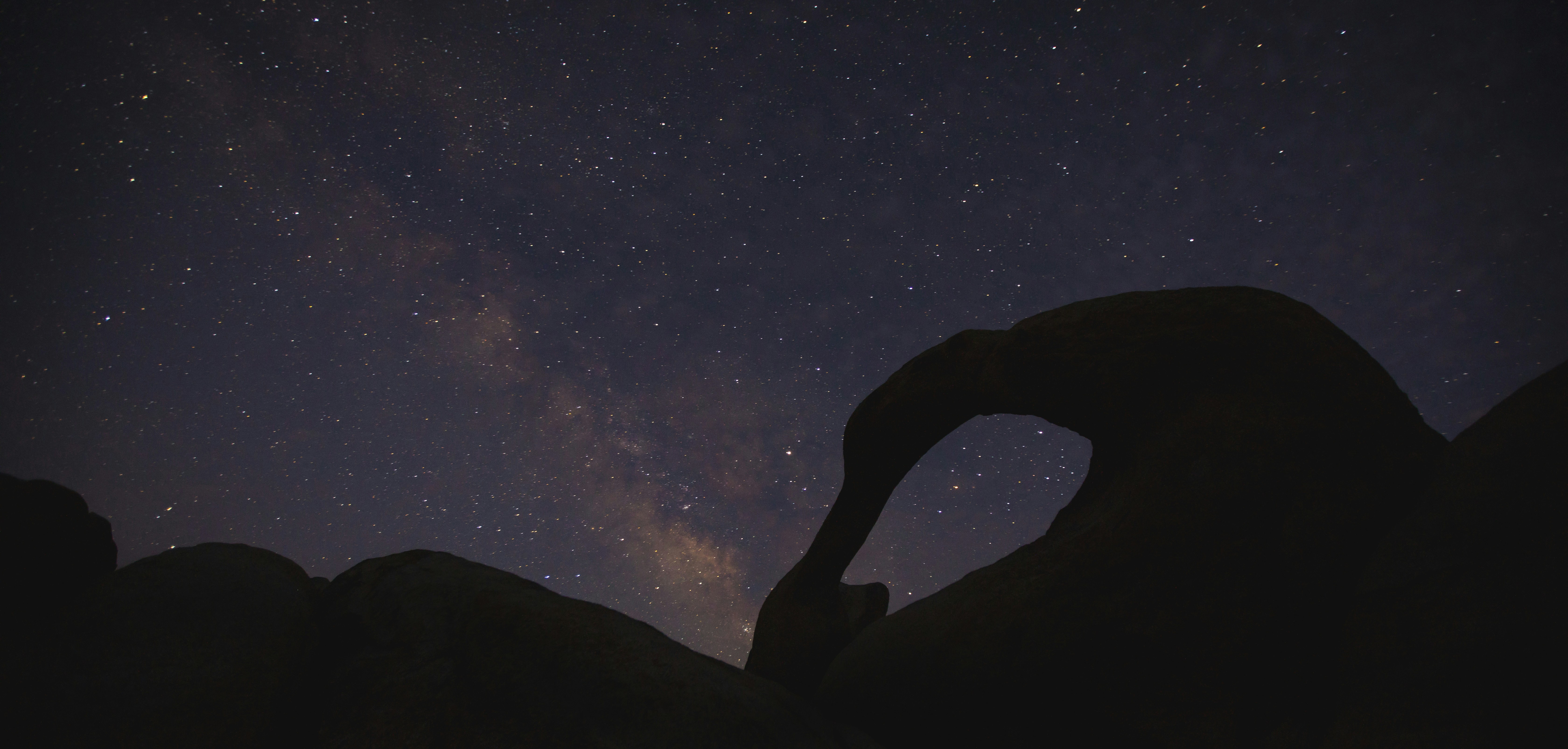 Silhouette of a natural arch against a starry night sky, showcasing the Milky Way's brilliance above.
