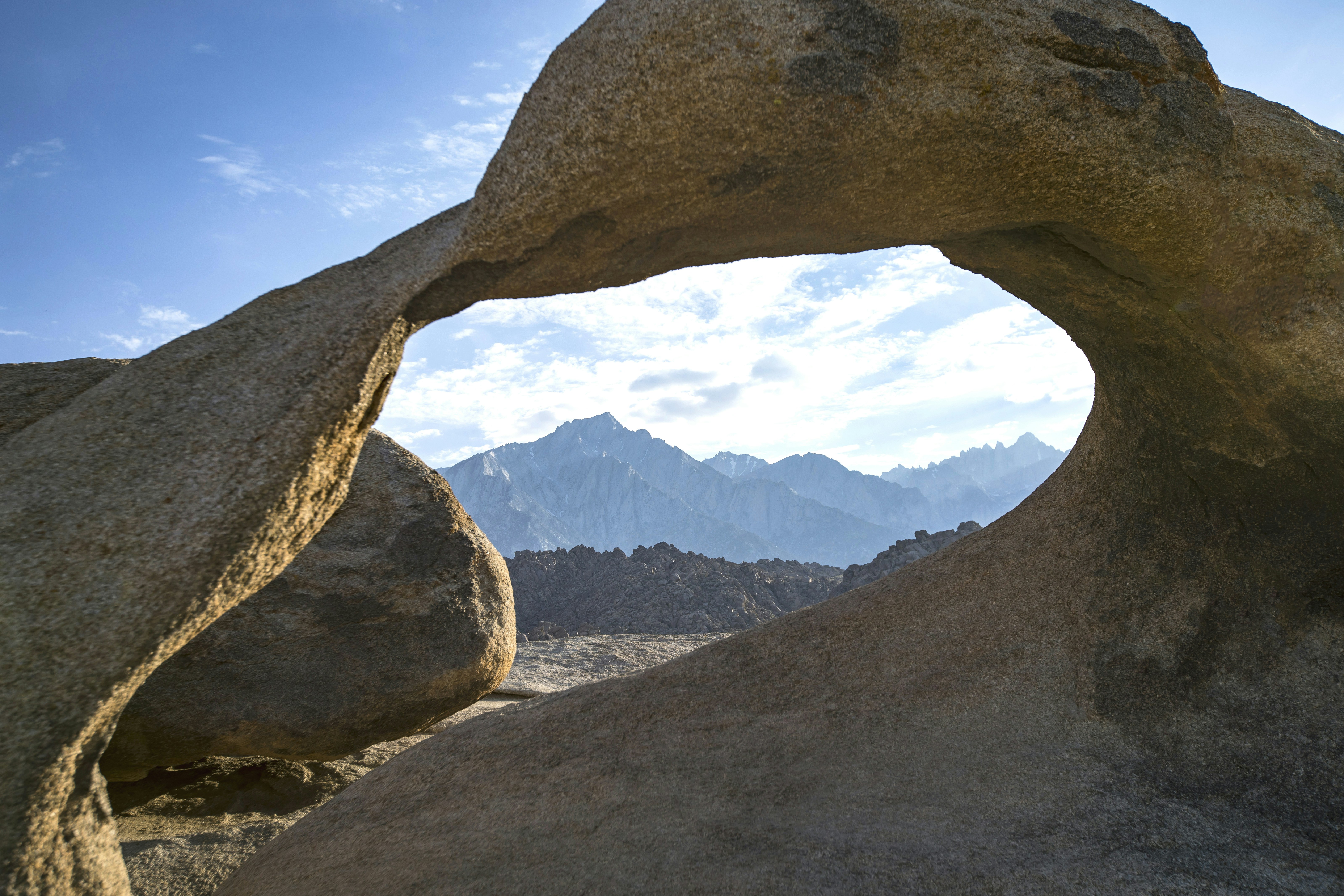 Rock arch framing distant mountain range under a blue sky.