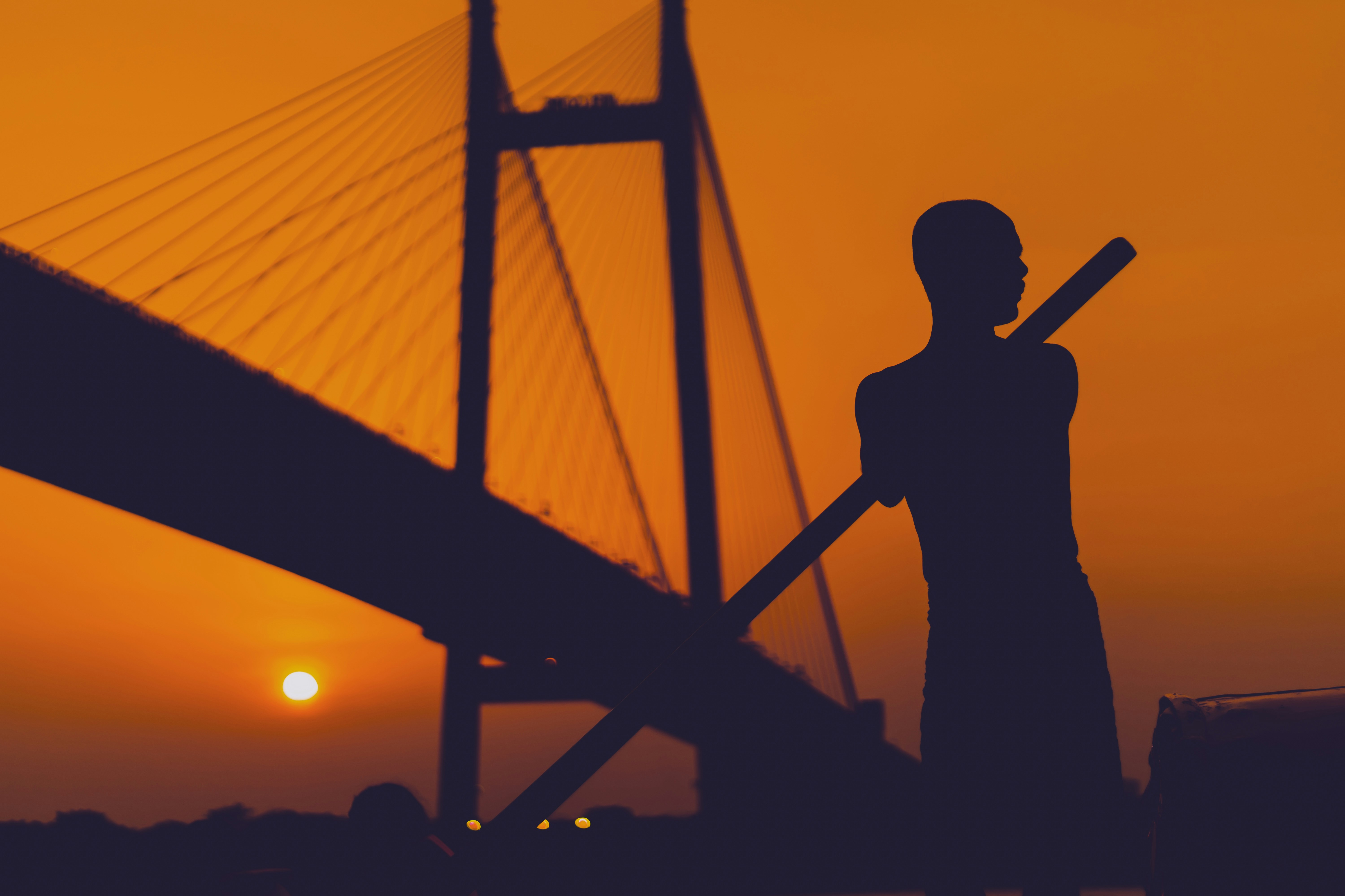 Silhouette at Sunset: A solitary figure with a cricket bat against a cable-stayed bridge