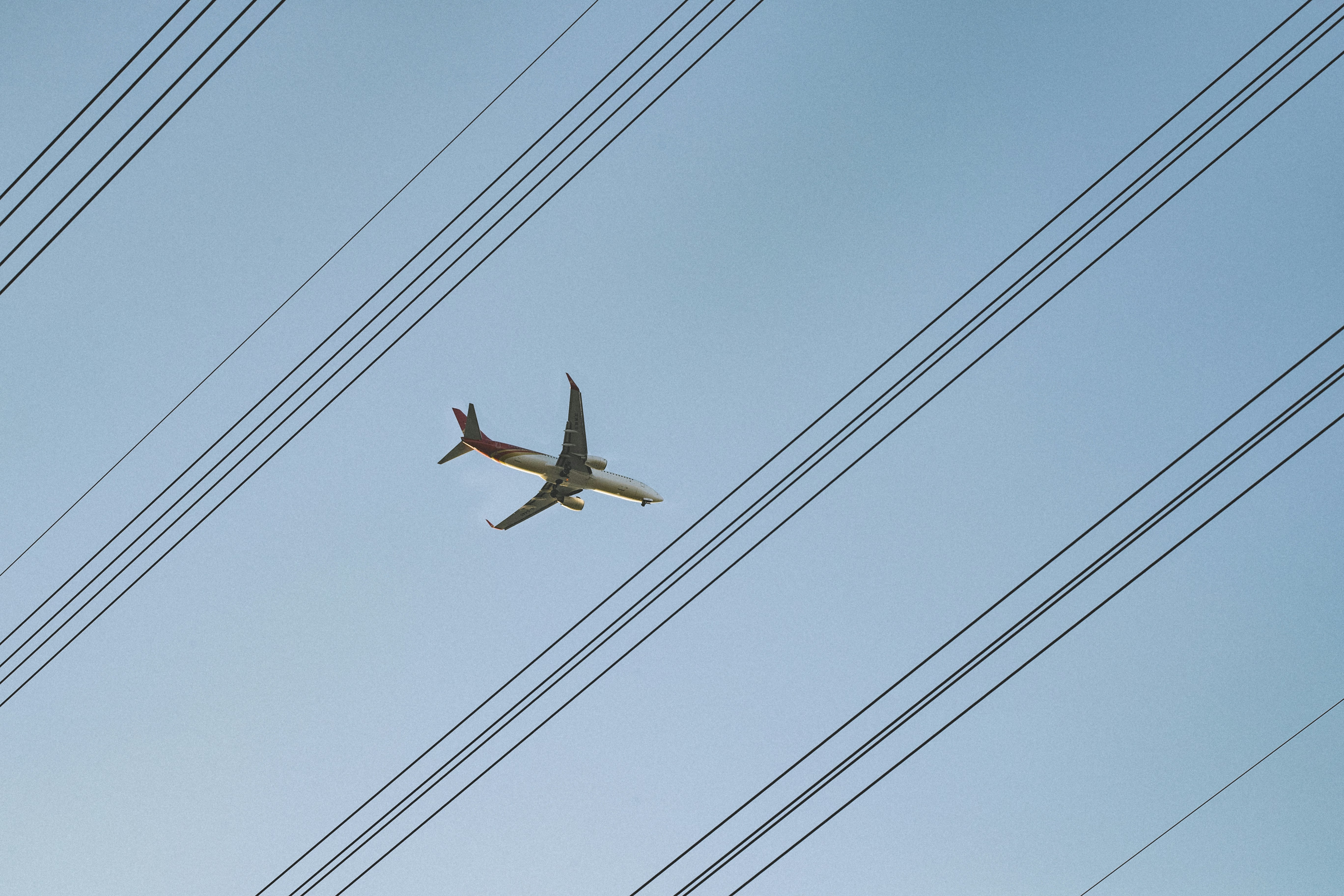 Commercial airplane flying above power lines against a clear blue sky.