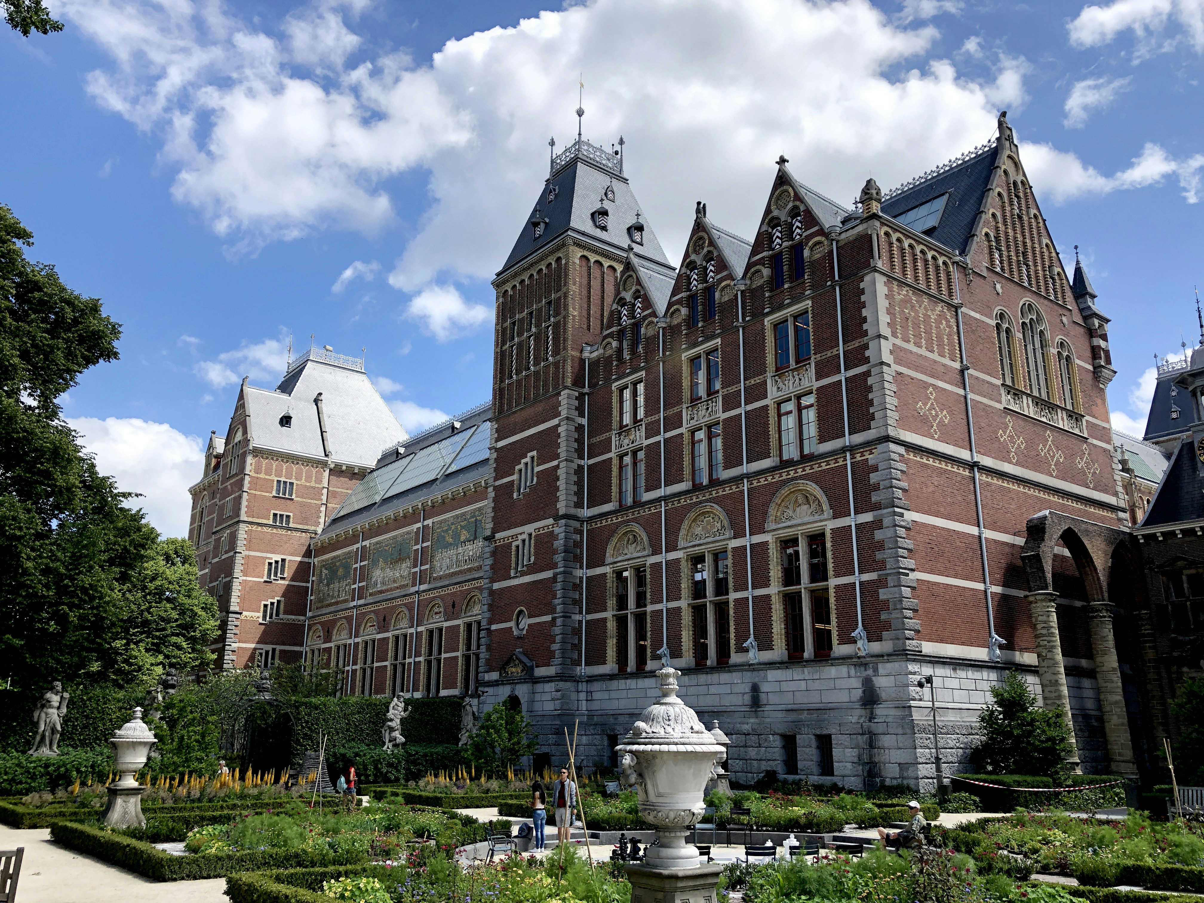 Historic museum building framed by lush gardens and vibrant flowers under a bright sky.