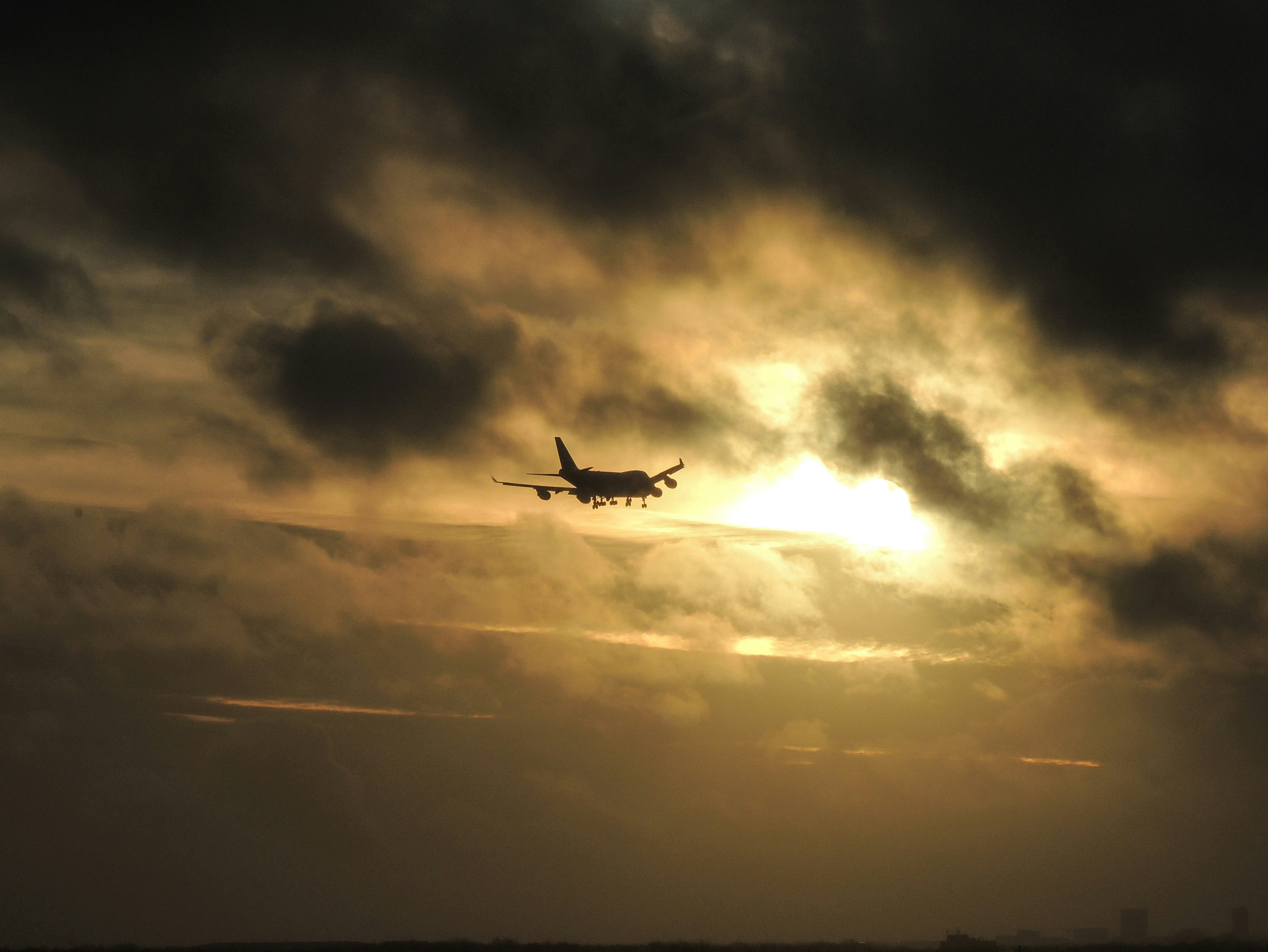 Airplane silhouetted against a dramatic sunset, with dark clouds framing the scene.