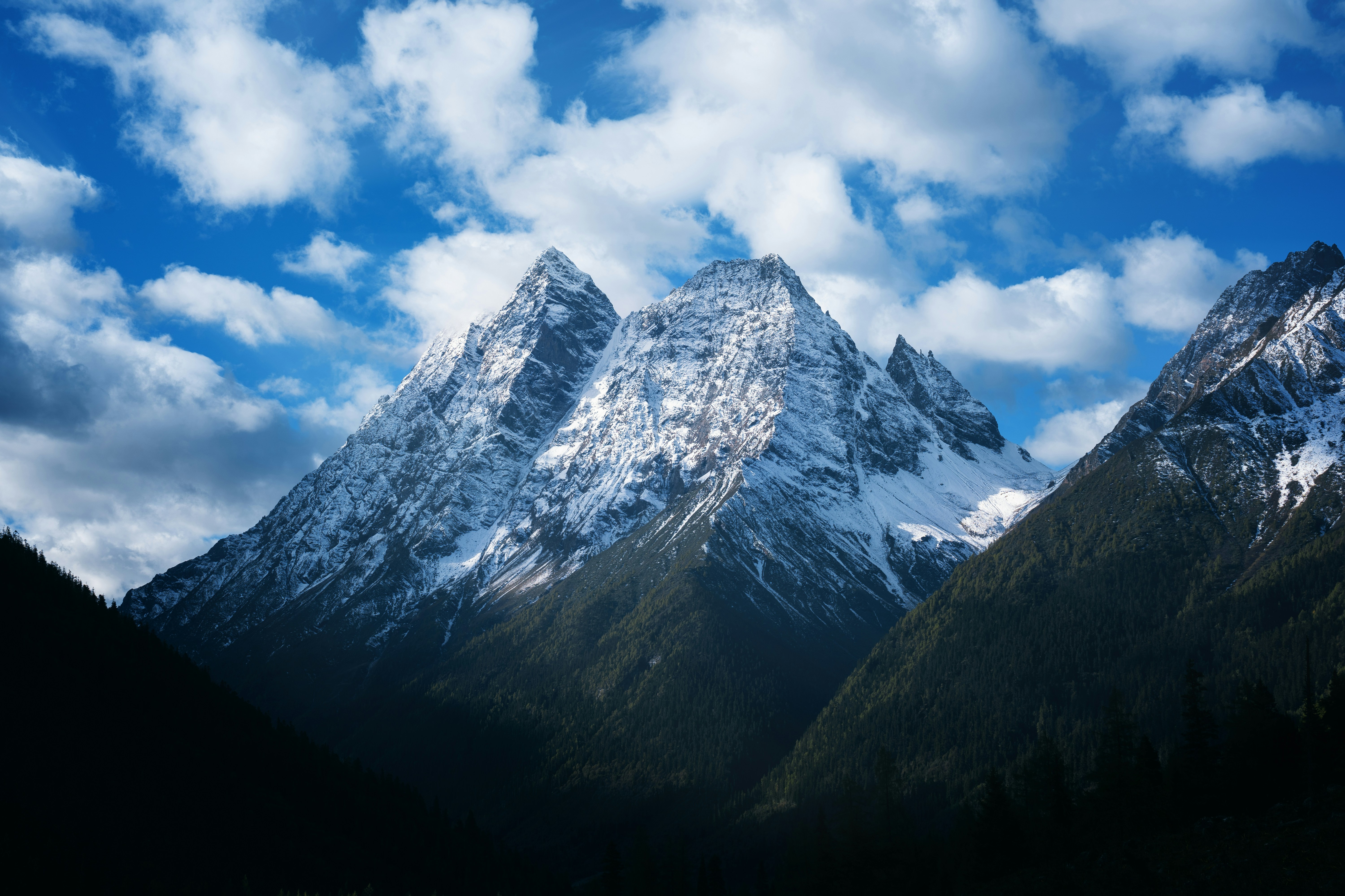 Snow-capped mountain peaks rise dramatically against a backdrop of vibrant clouds, showcasing the grandeur of nature's landscape.