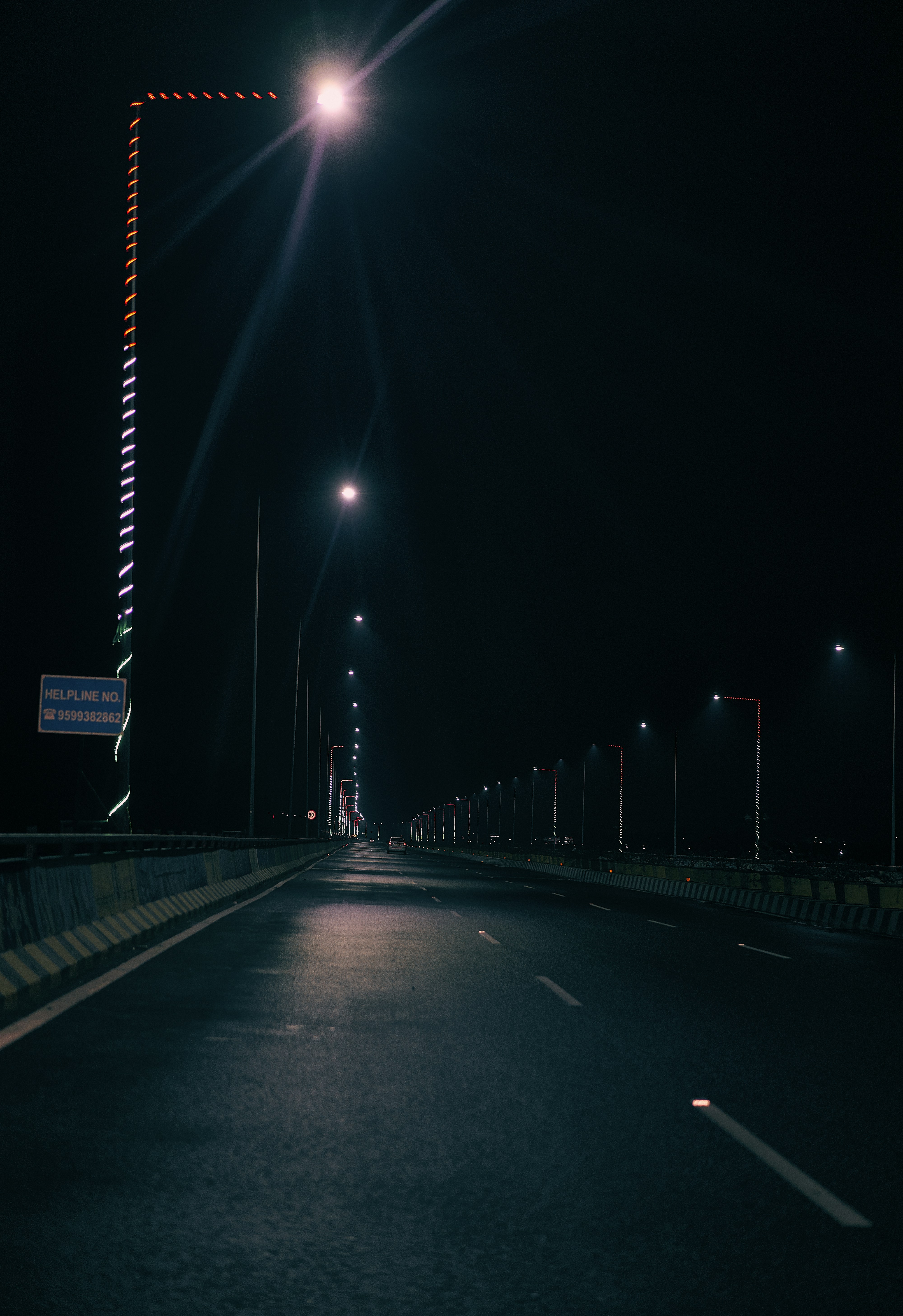 Vibrant streetlights line a deserted road at night, creating a mesmerizing visual path. The scene captures the interplay of light and shadow in a tranquil urban setting.