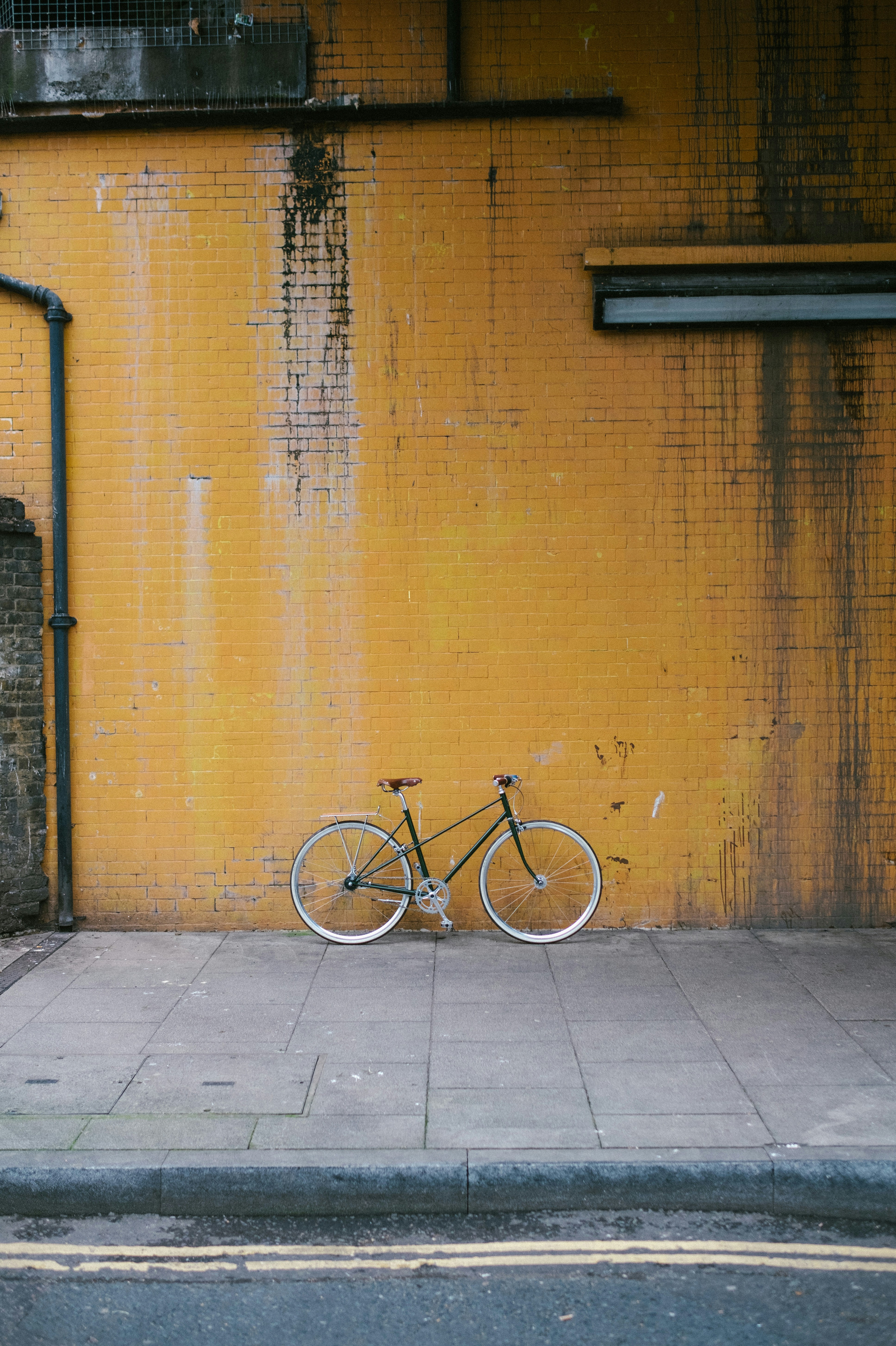A solitary bicycle rests against a vibrant yellow wall, showcasing urban life and color contrast.