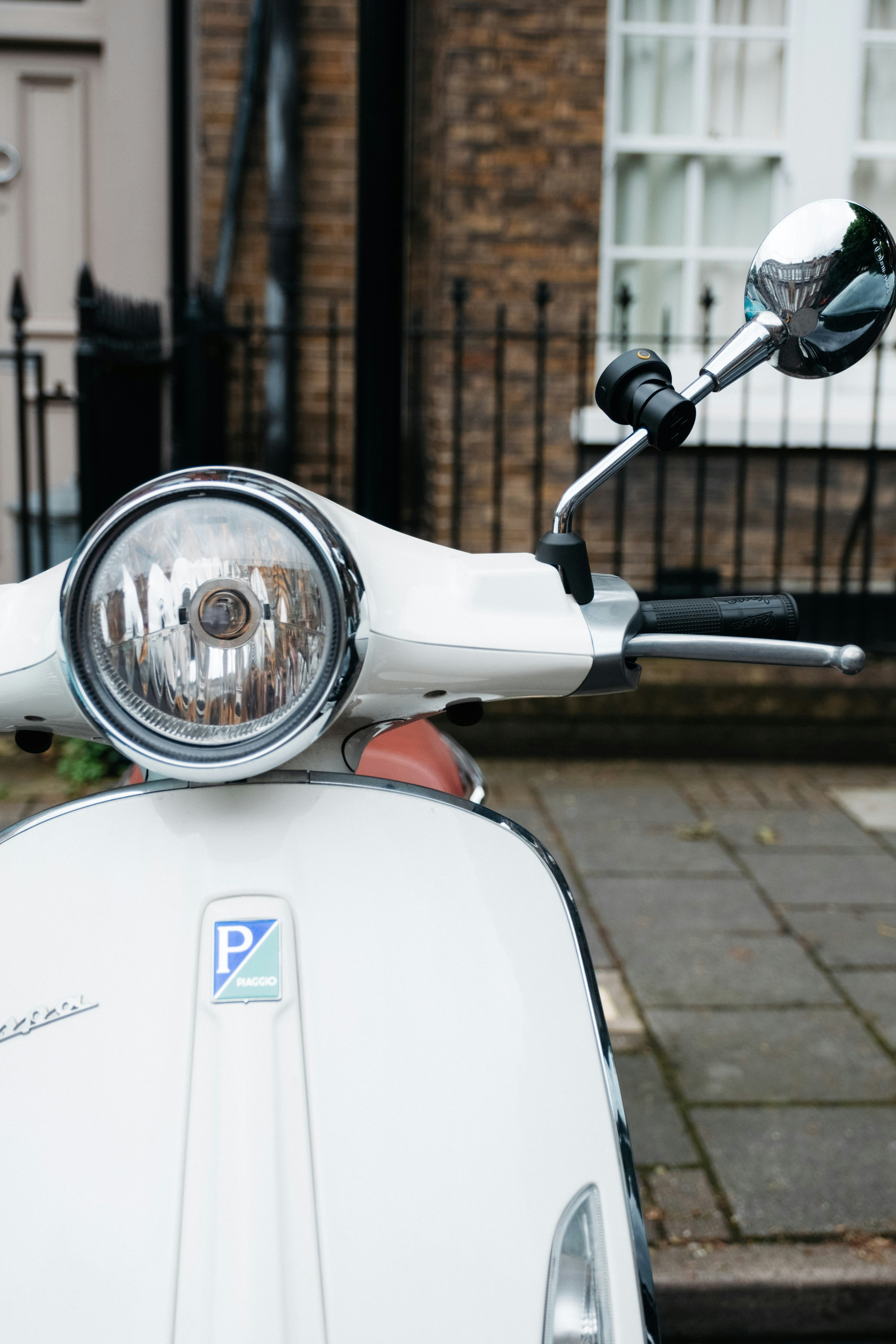 Close-up of a white Vespa scooter with a round headlight and rearview mirror, set against a brick wall in London.