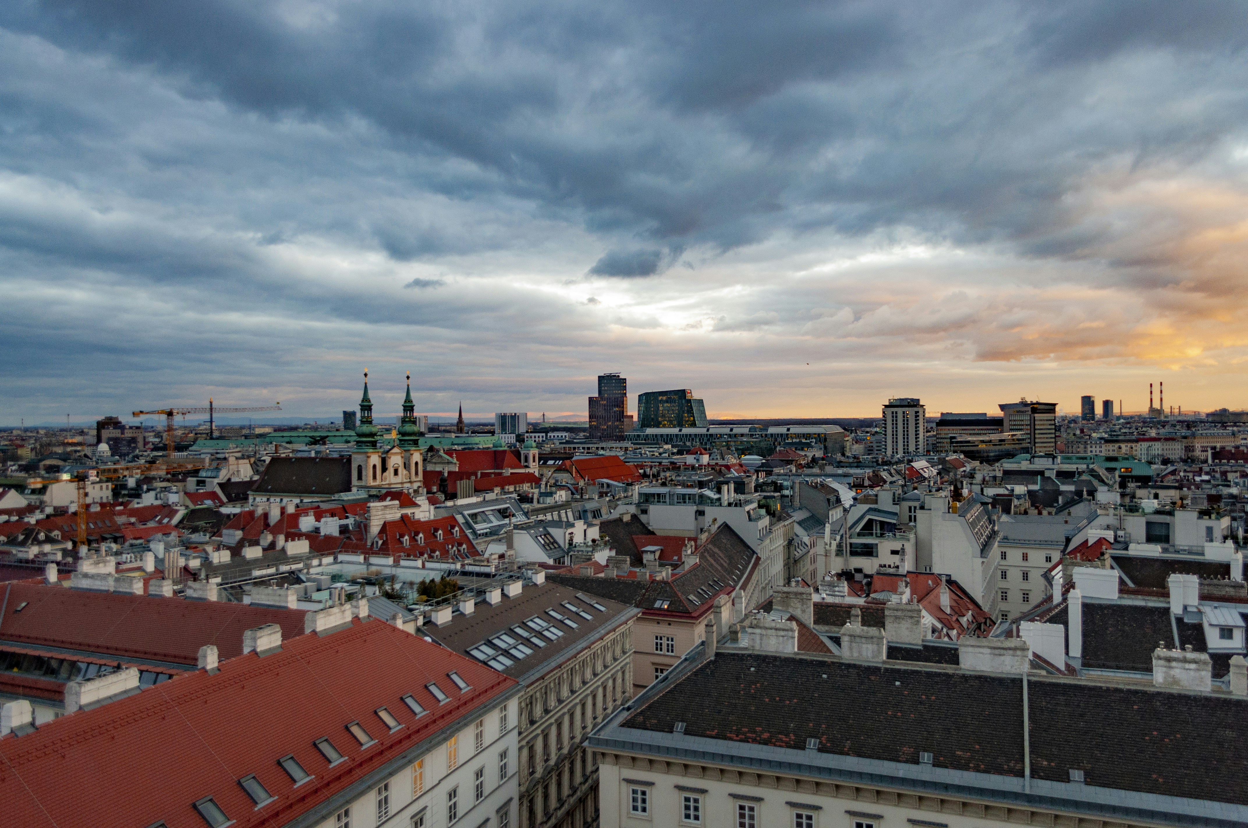 Aerial view of Vienna's rooftops under dramatic clouds at sunset.
