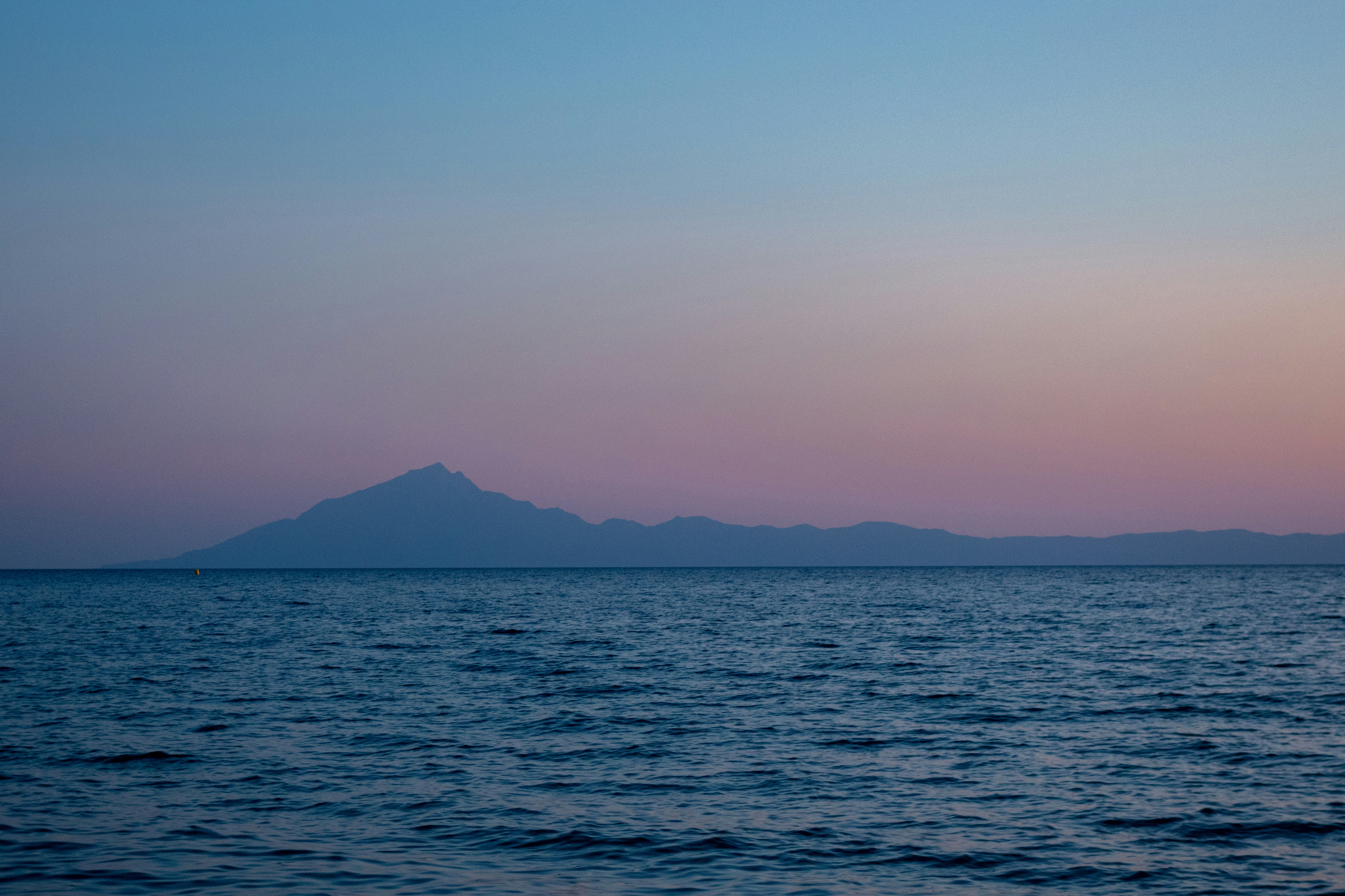 Distant mountain silhouette against a pastel-colored sunset sky over calm ocean waters.
