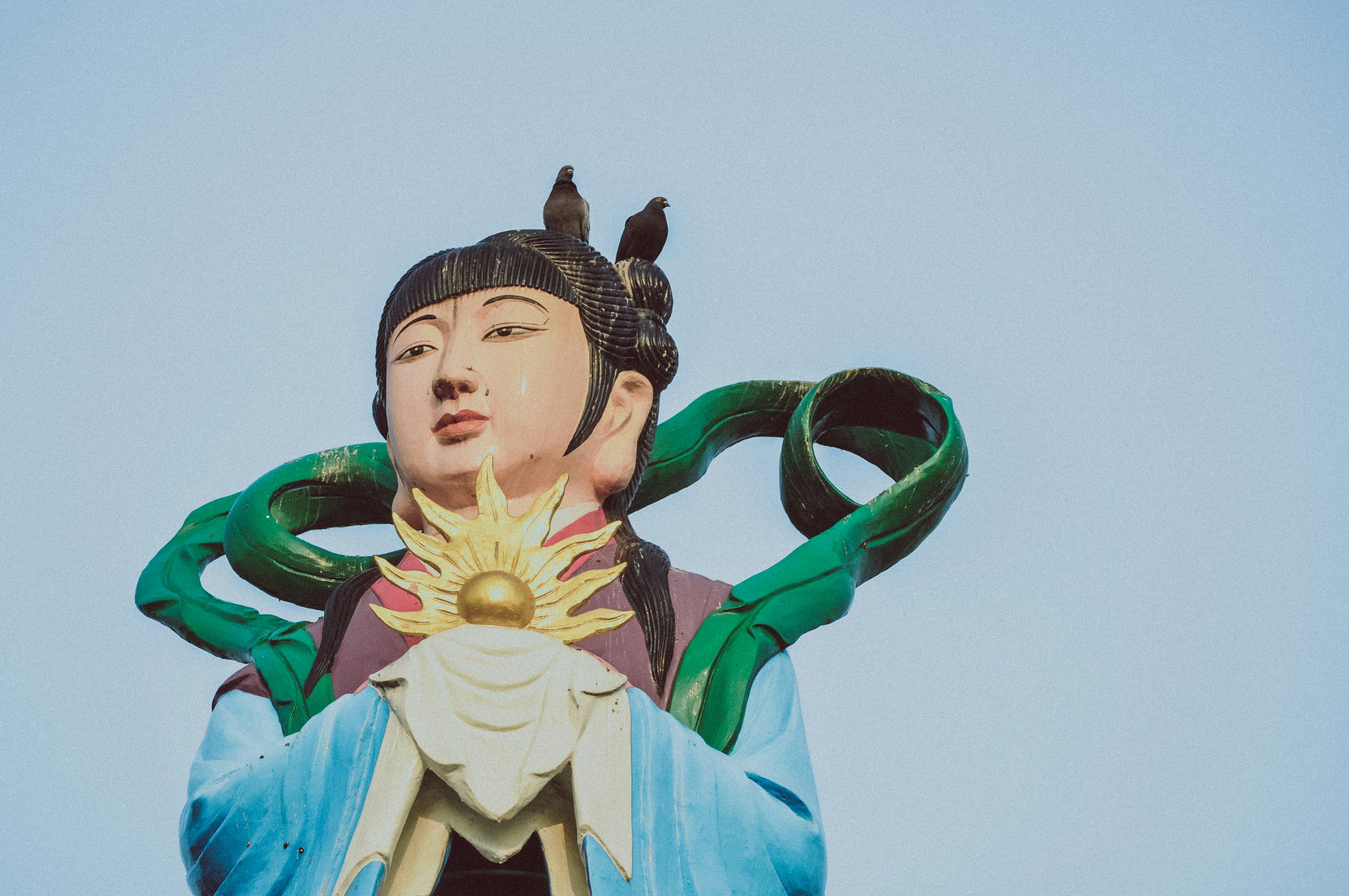 Colorful statue of a serene figure holding a sun emblem against a clear blue sky.