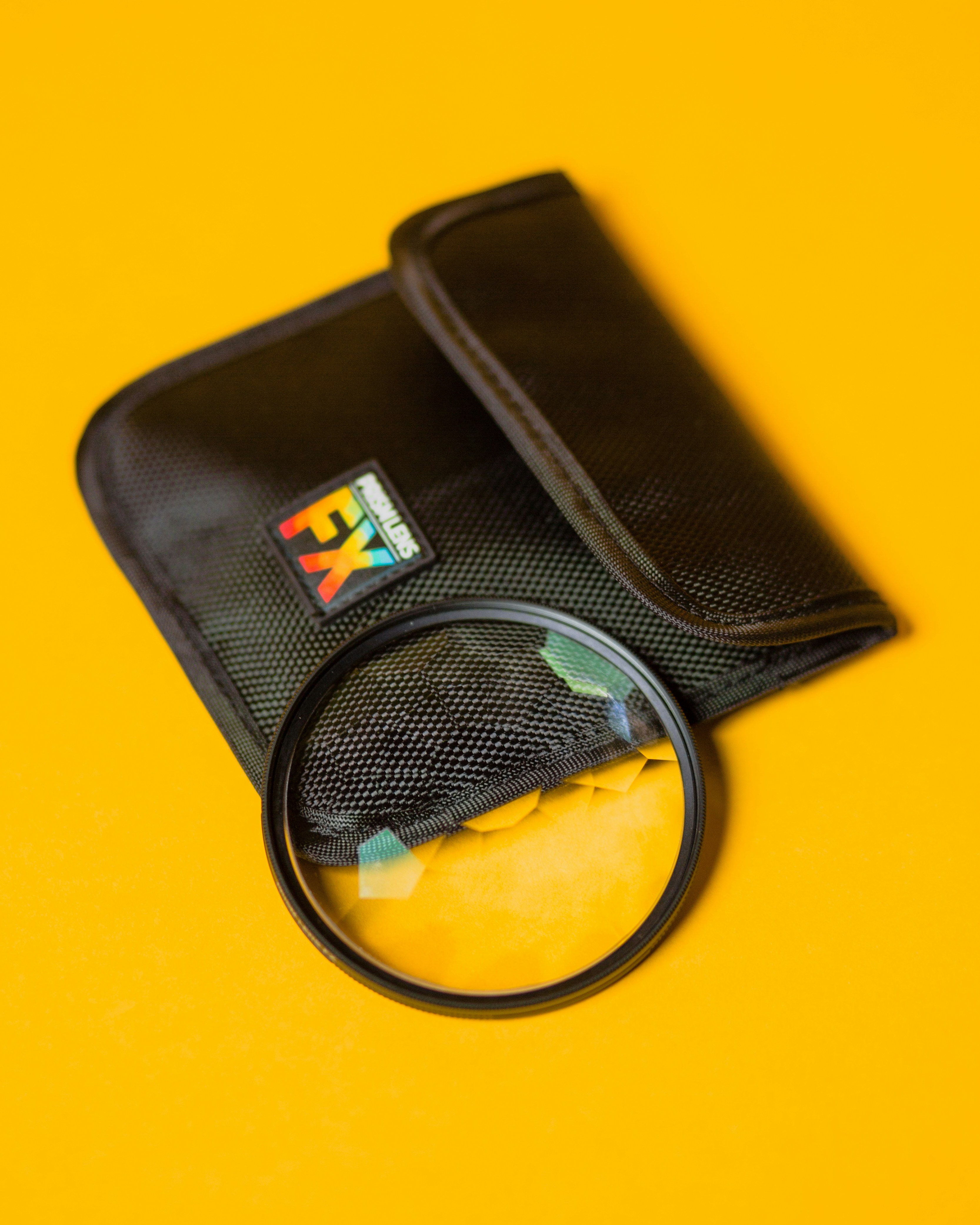 Black textured wallet with an FX logo sits on a vivid yellow background, magnified by a circular lens to reveal its weave.