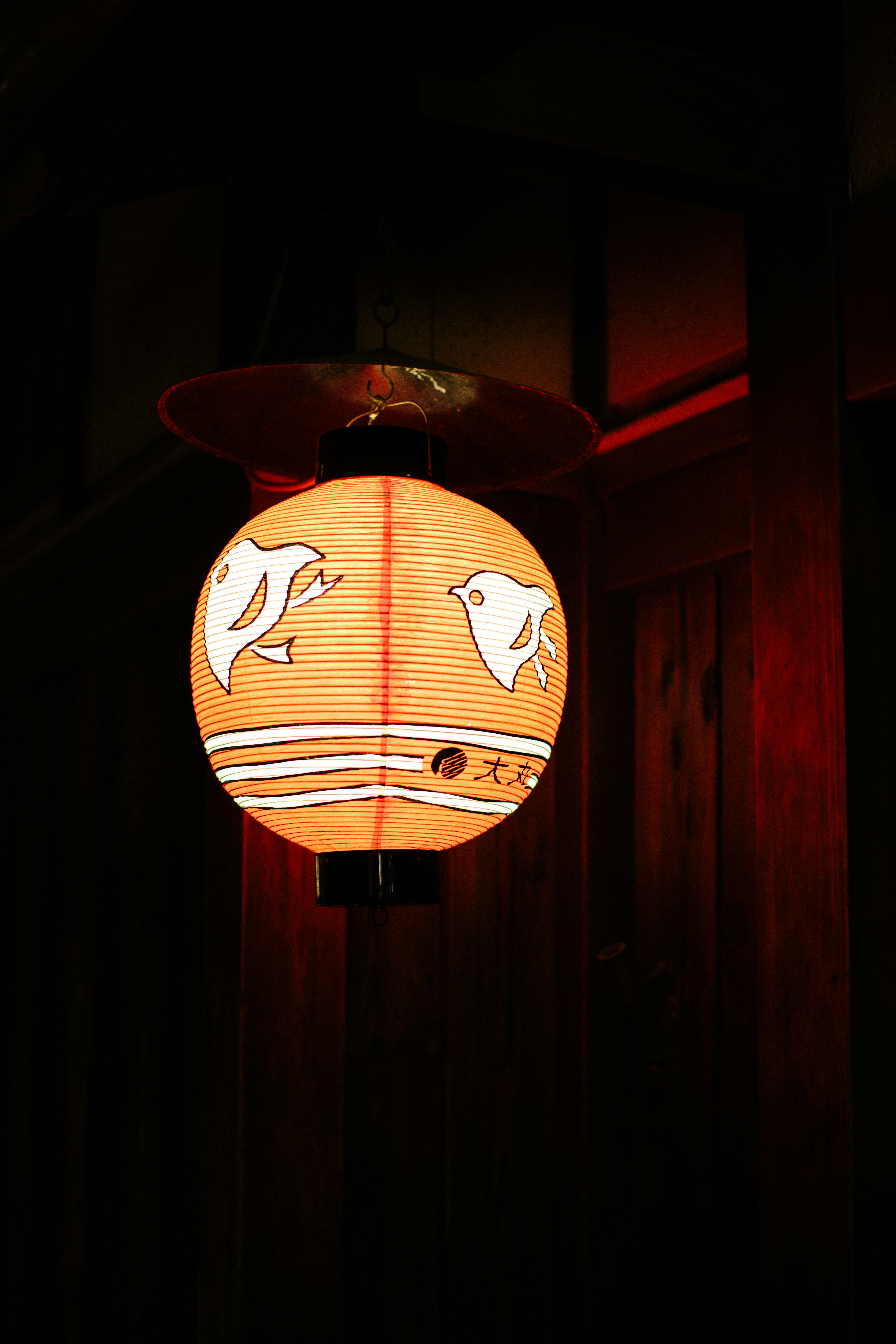 Traditional lantern adorned with fish motifs, casting a warm glow against a wooden backdrop.