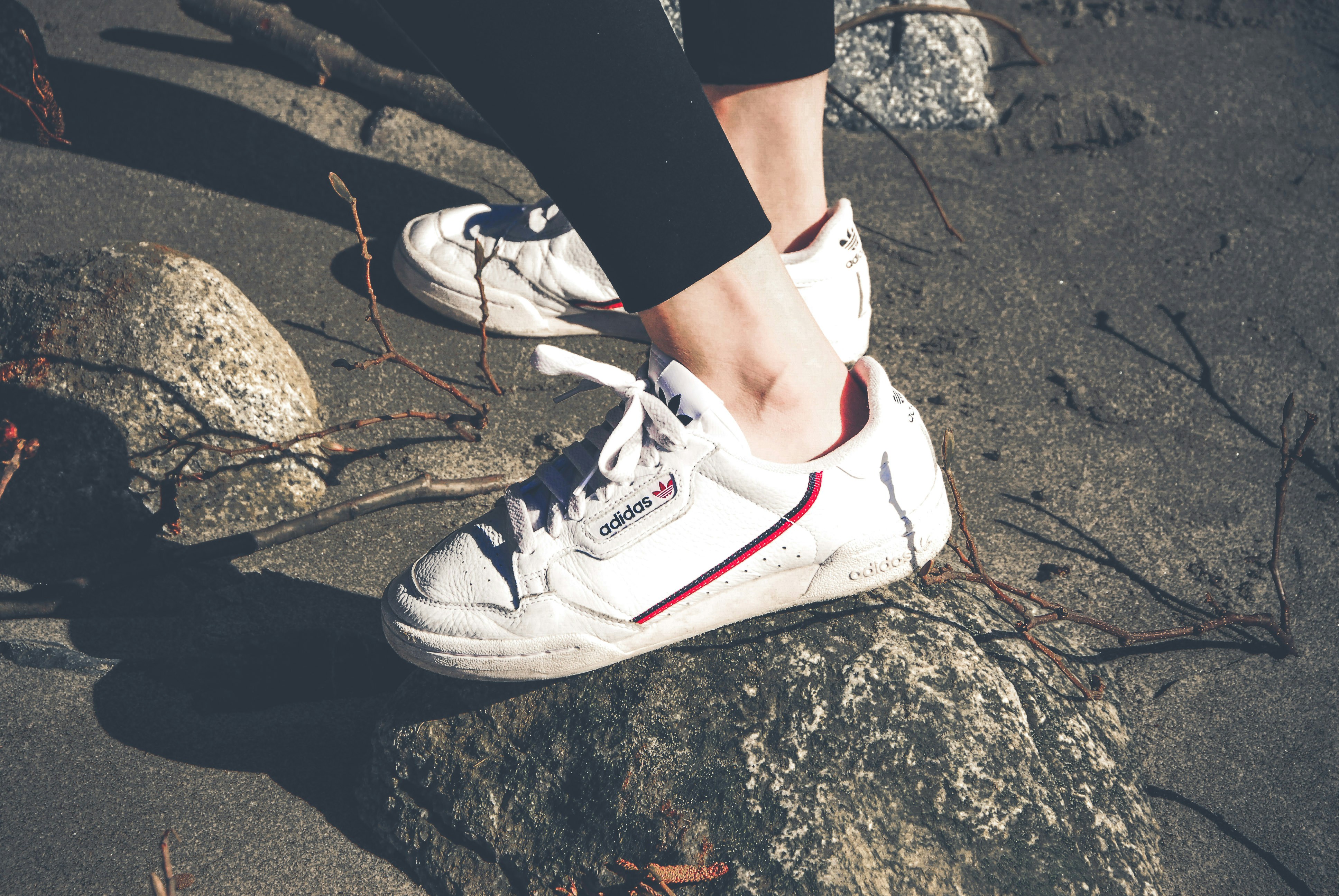 Stride on the Dark Shore: White Sneakers on Weathered Rocks