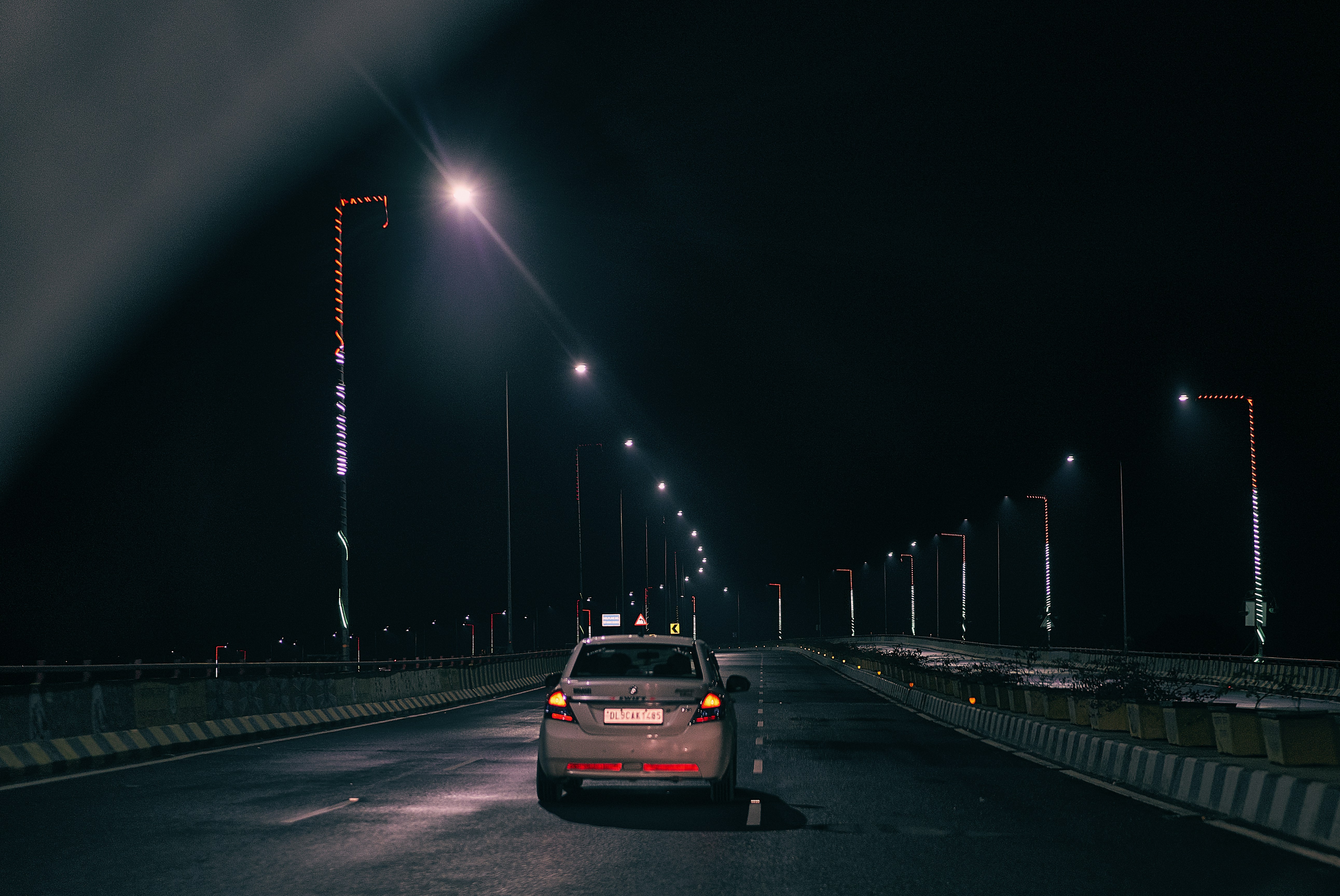 A car drives down a dimly lit highway adorned with vibrant streetlights, creating a striking contrast against the night sky.