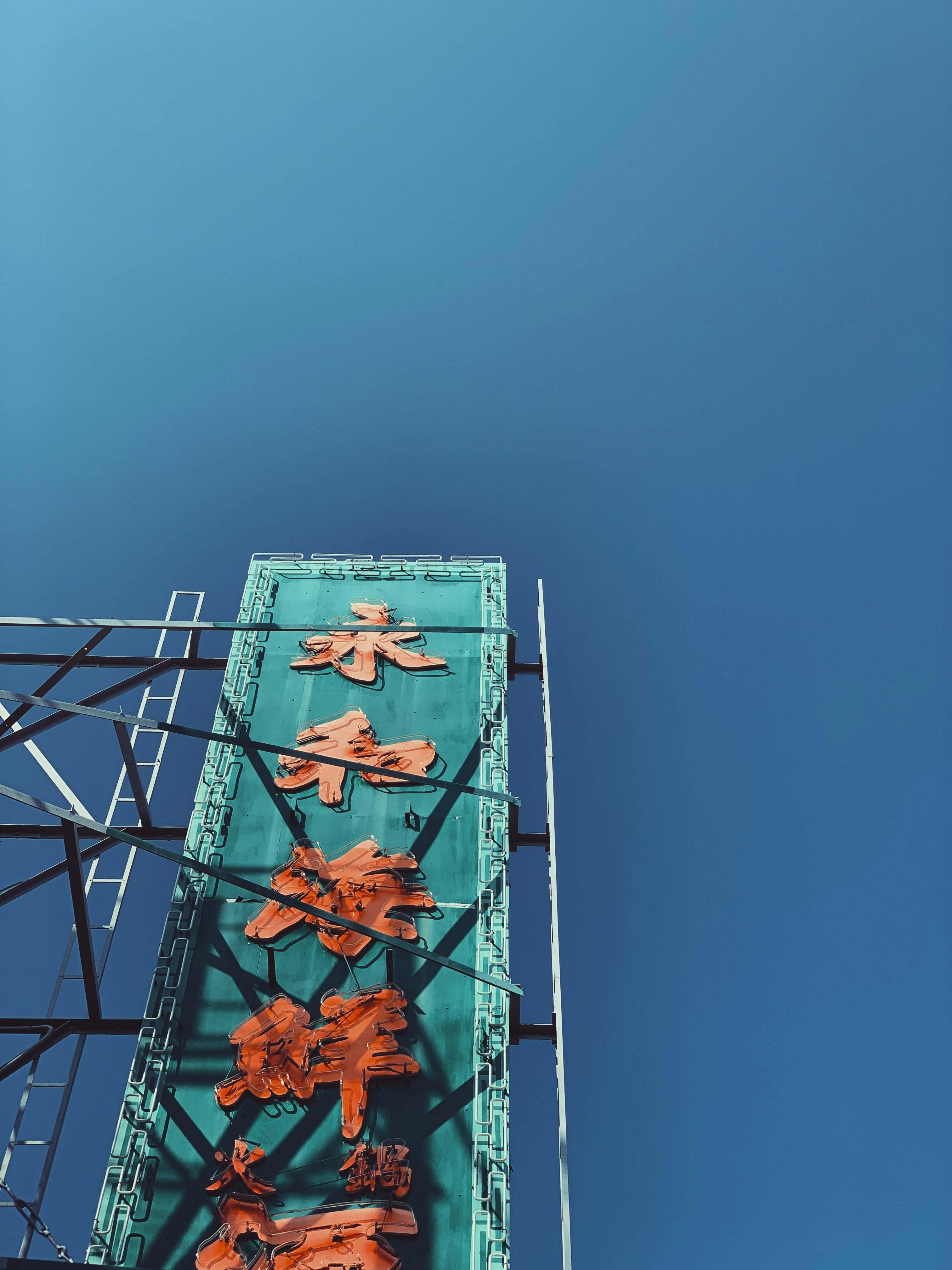 Teal Vertical Signboard Rising from Steel Lattice Under a Vast Blue Sky