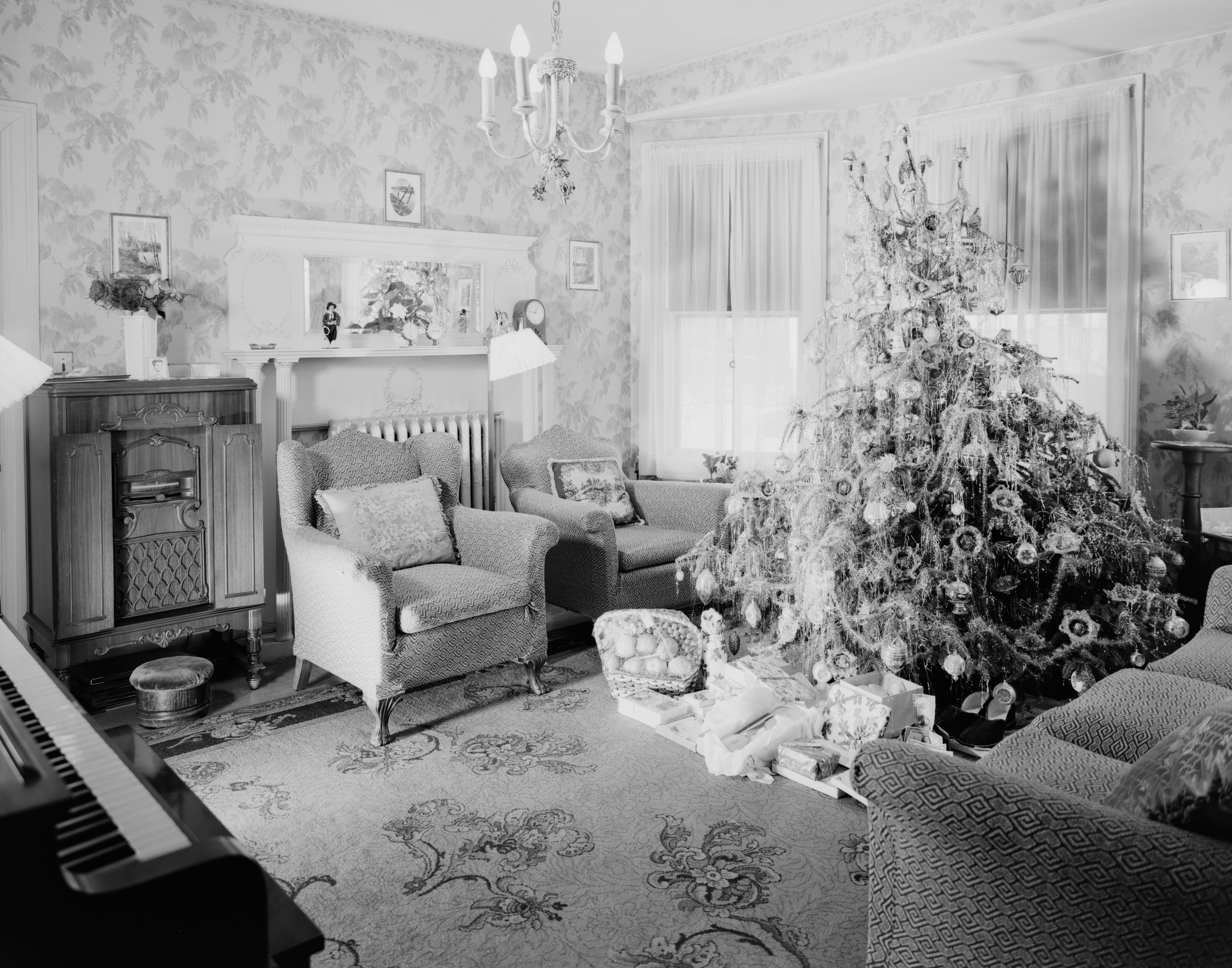 Ornately decorated Christmas tree in a vintage living room with patterned wallpaper and classic furniture.