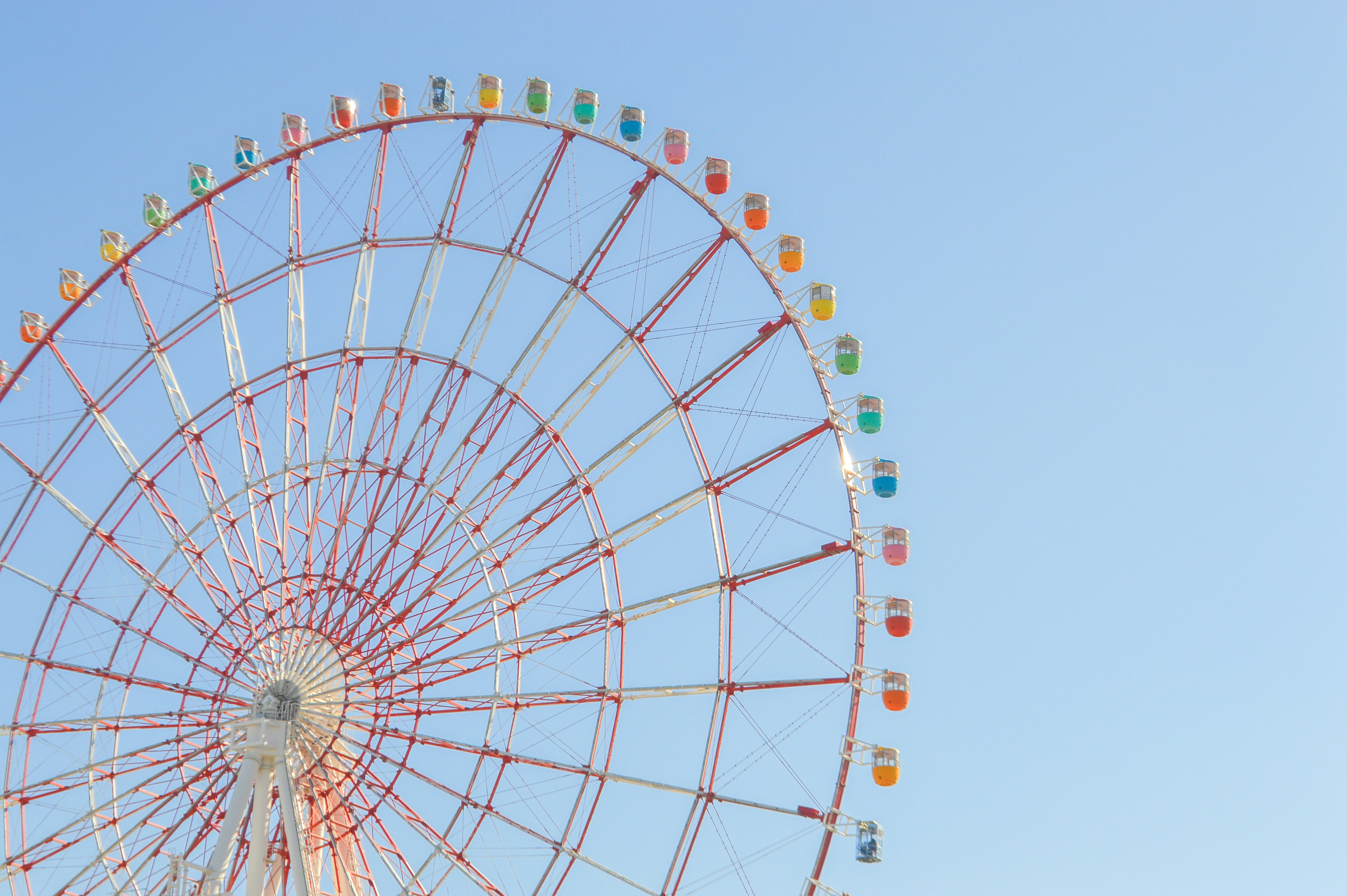 A vibrant ferris wheel adorned with colorful cabins spins against a clear blue sky.